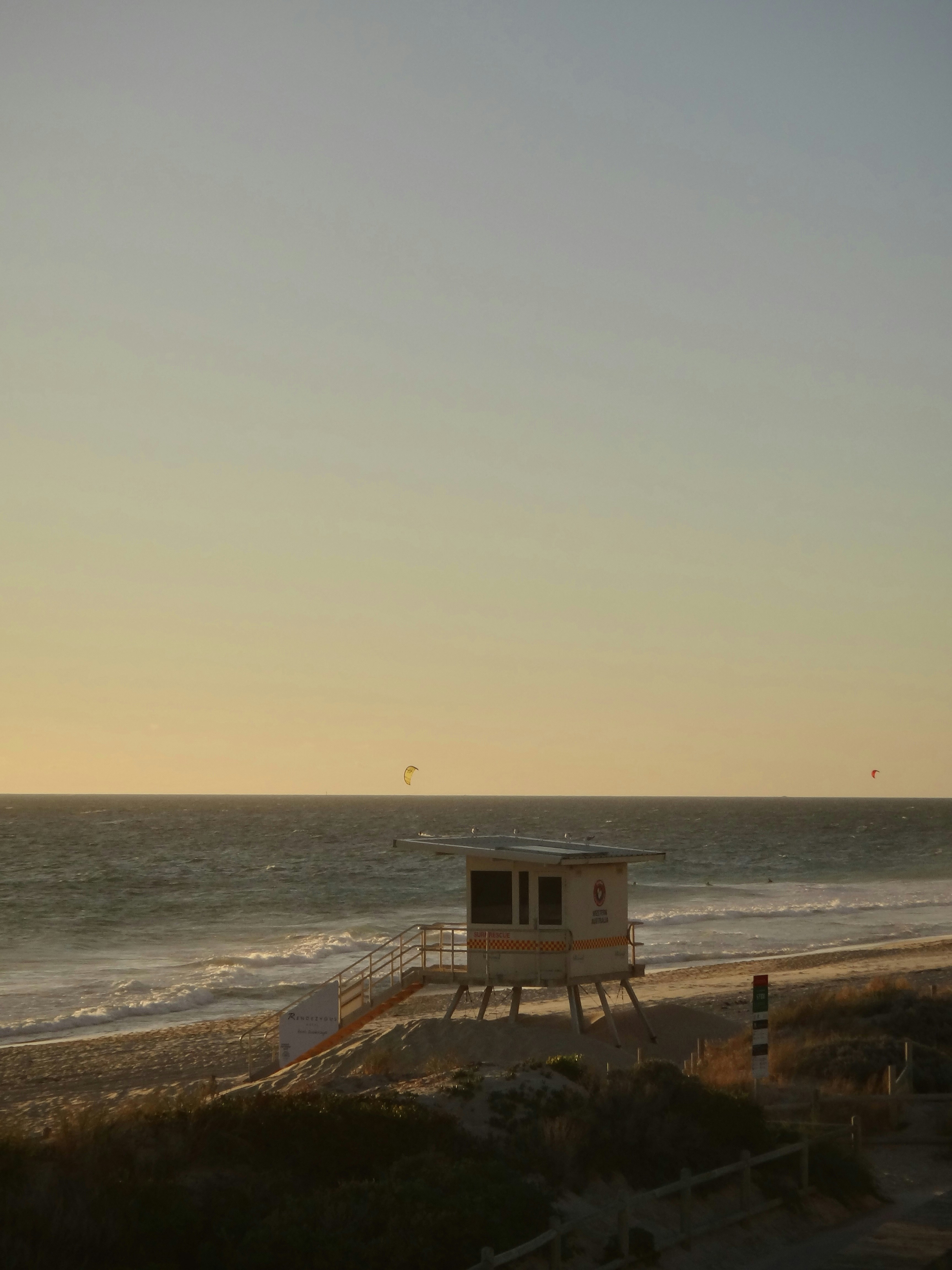 Lifeguard station overlooking the ocean at sunset, with colorful kites in the distance. The tranquil scene captures the essence of coastal life.