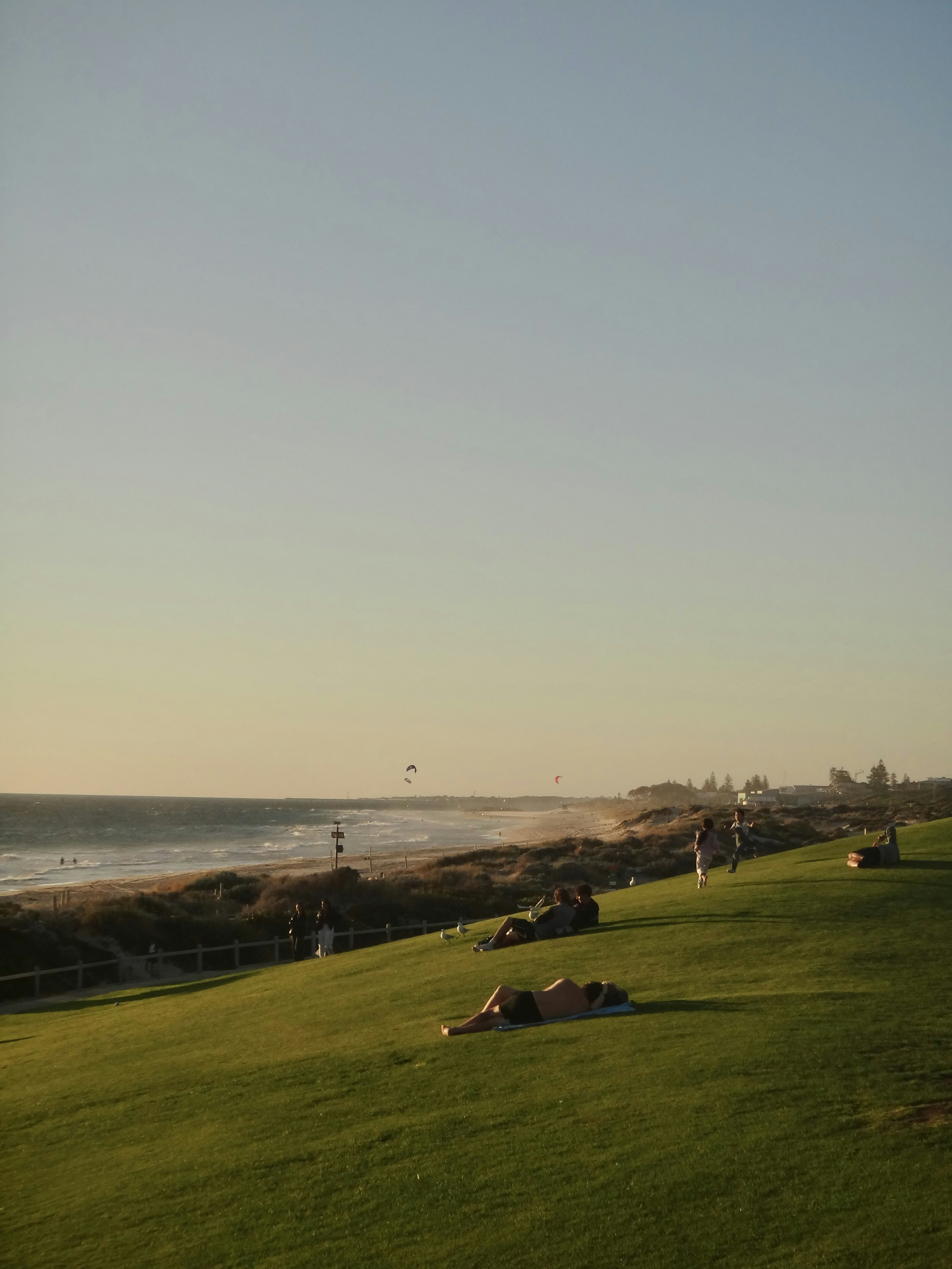 People are relaxing on a grassy hill near the beach.