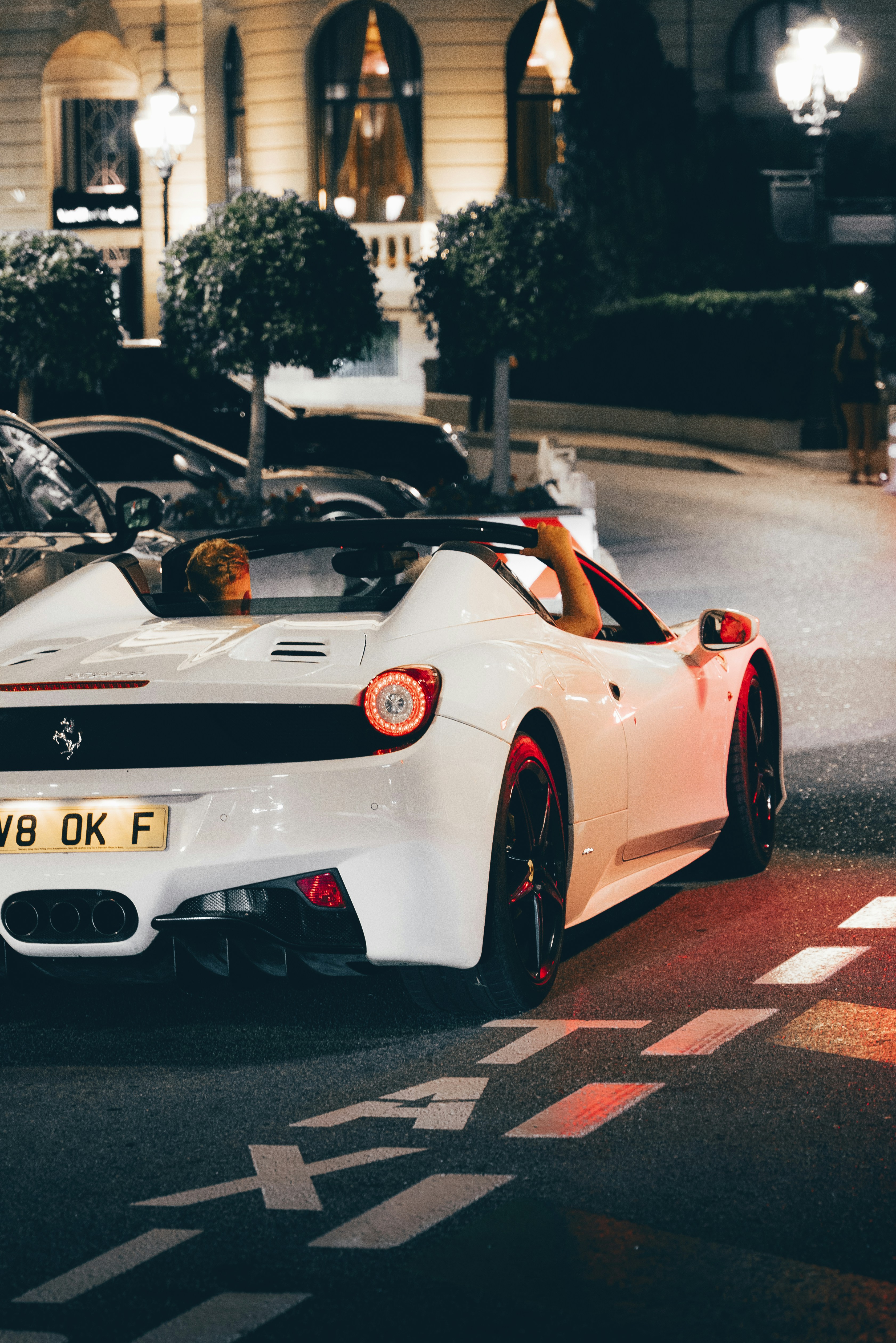 A sleek white Ferrari convertible parked on a city street, illuminated by ambient streetlights. The luxury vehicle's design and details are highlighted against the nighttime backdrop.