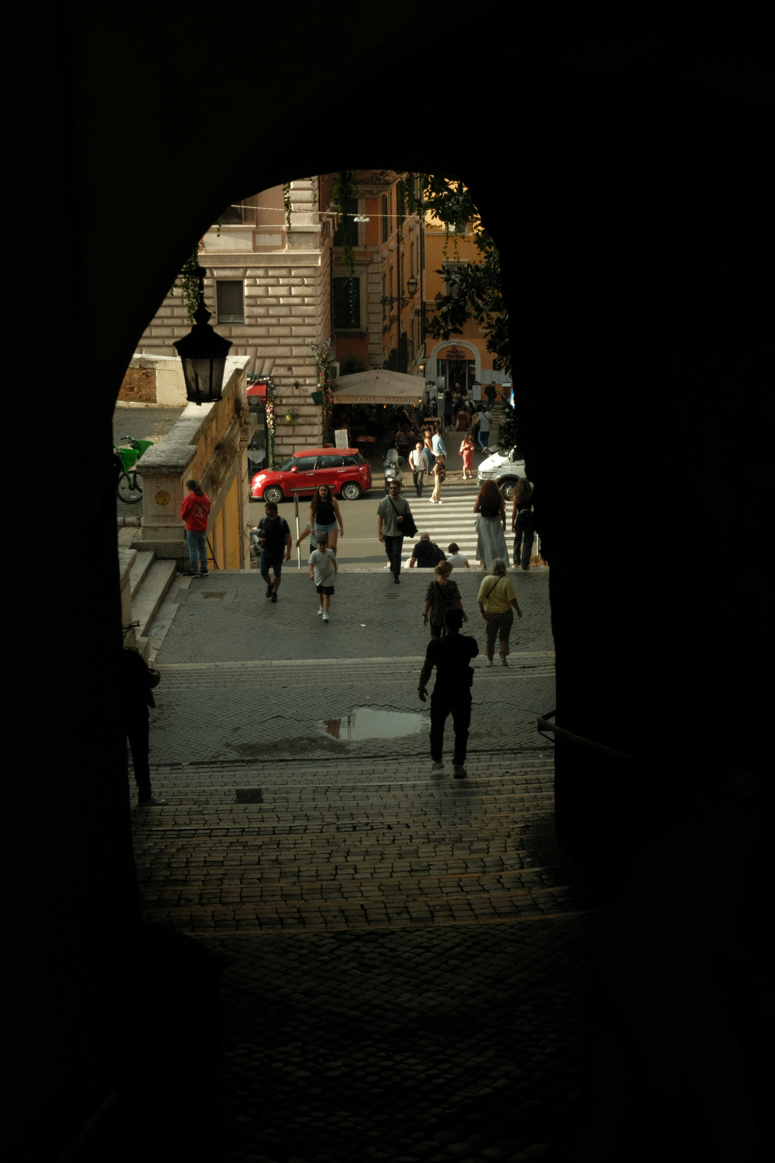 Rome streets | People walk down stairs framed by a dark archway.