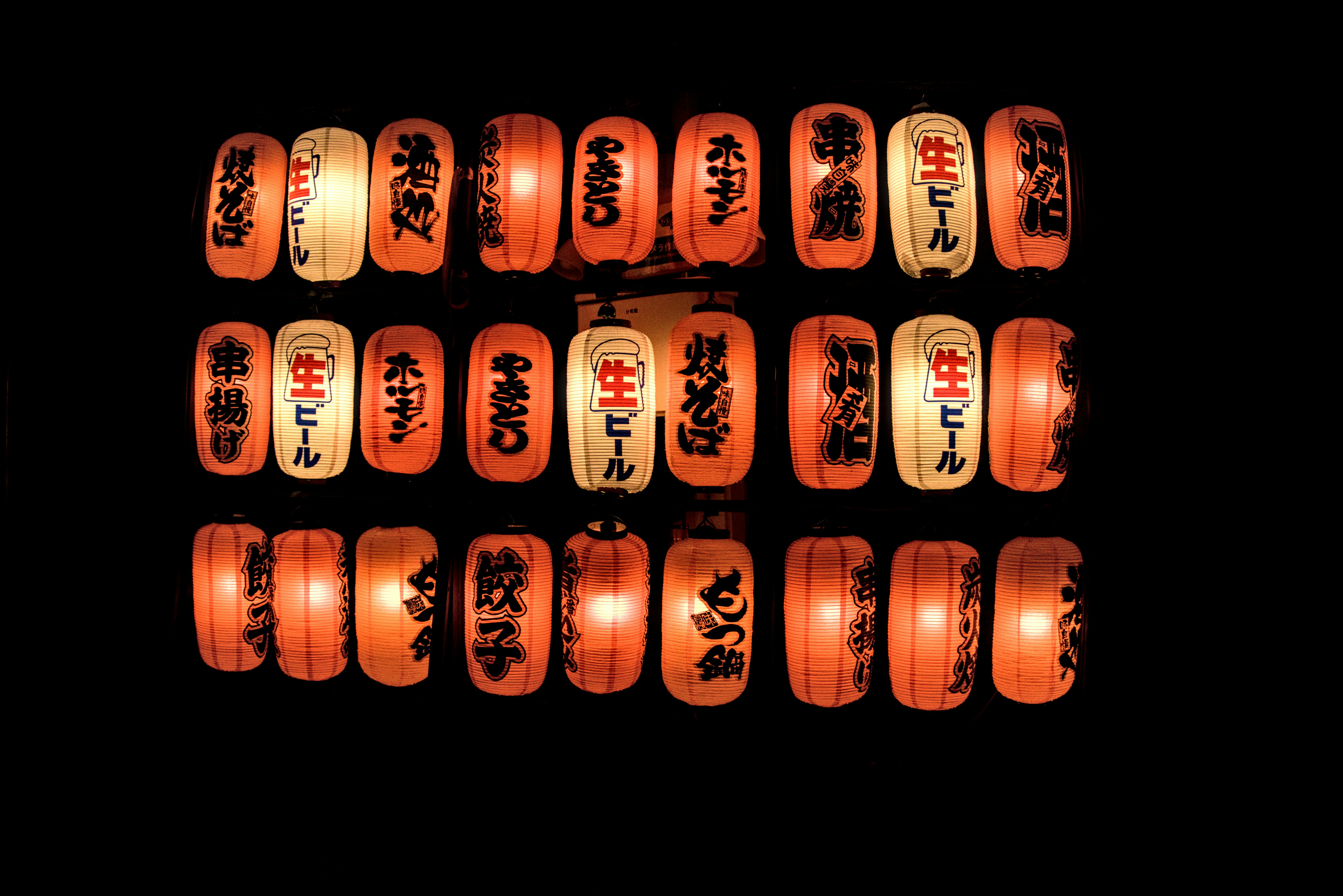 A vibrant display of traditional Japanese lanterns, each adorned with unique calligraphy, glowing against a dark backdrop.