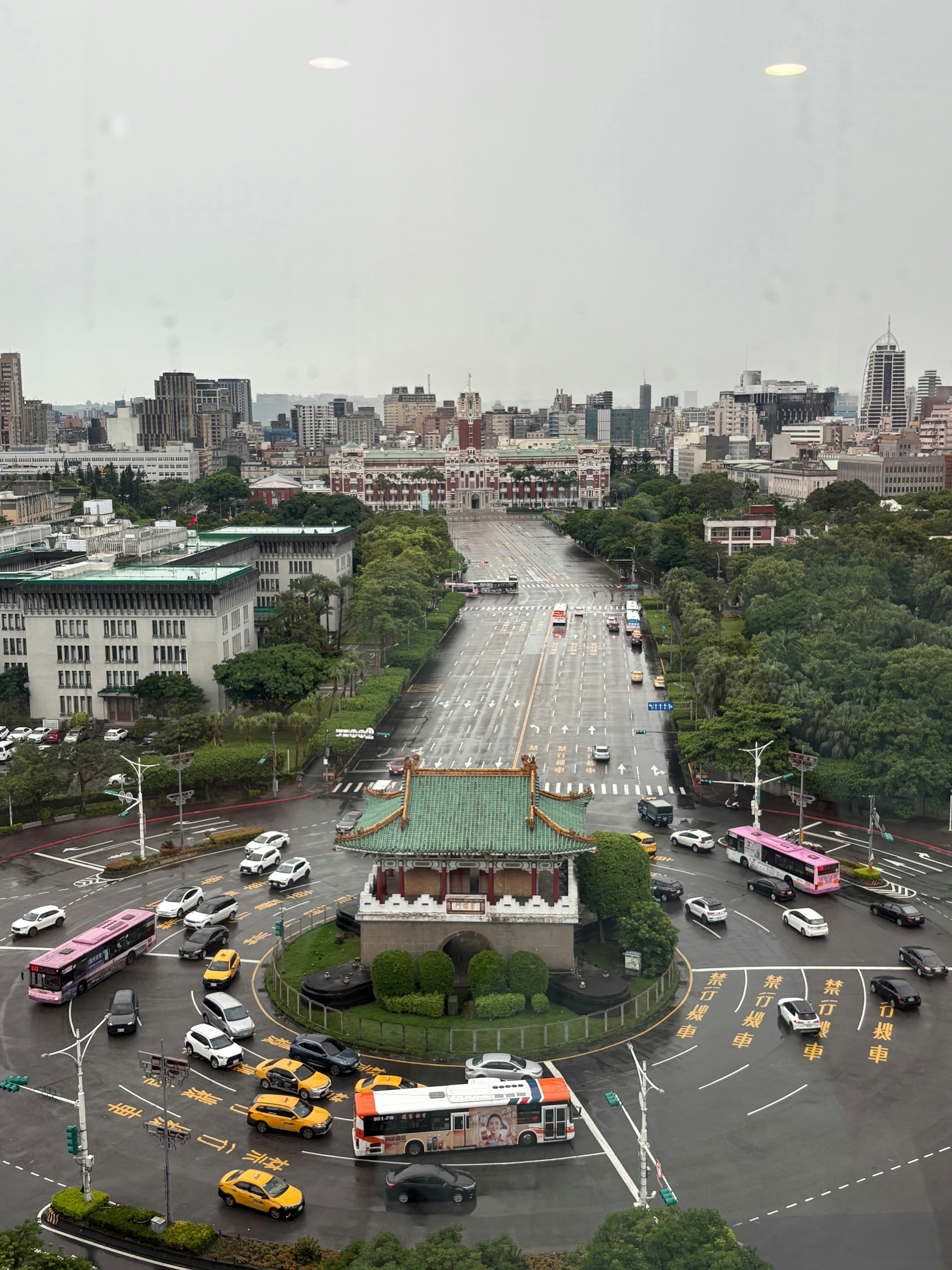 City view, roundabout with wide road straight along to the building ,it feels like you’re controlling those cars and buses ,wailing where they would go? | A bird's-eye view of a city street.