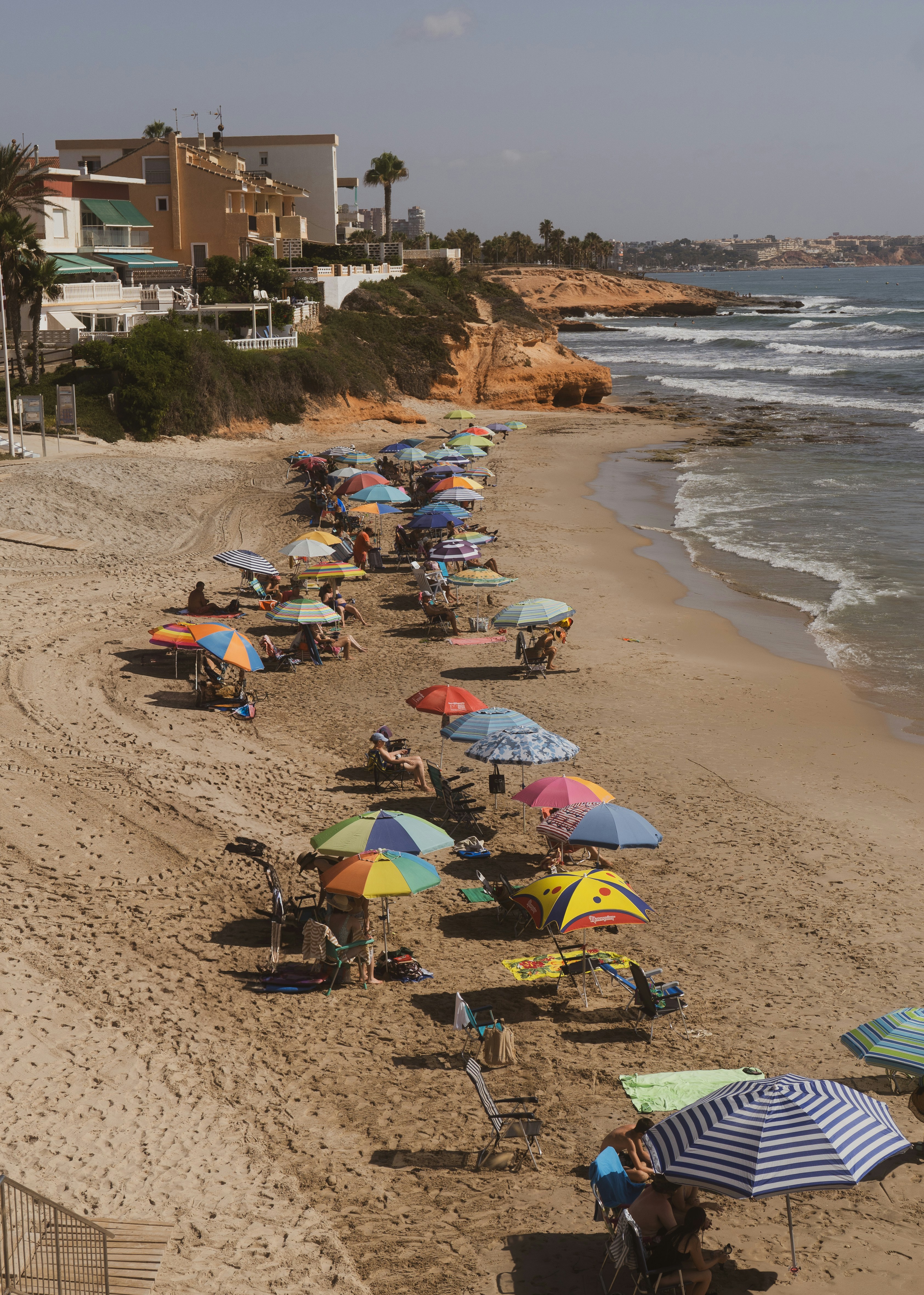Sunny umbrellas on the beach. | Beachgoers relax under umbrellas along a sunny coastline.