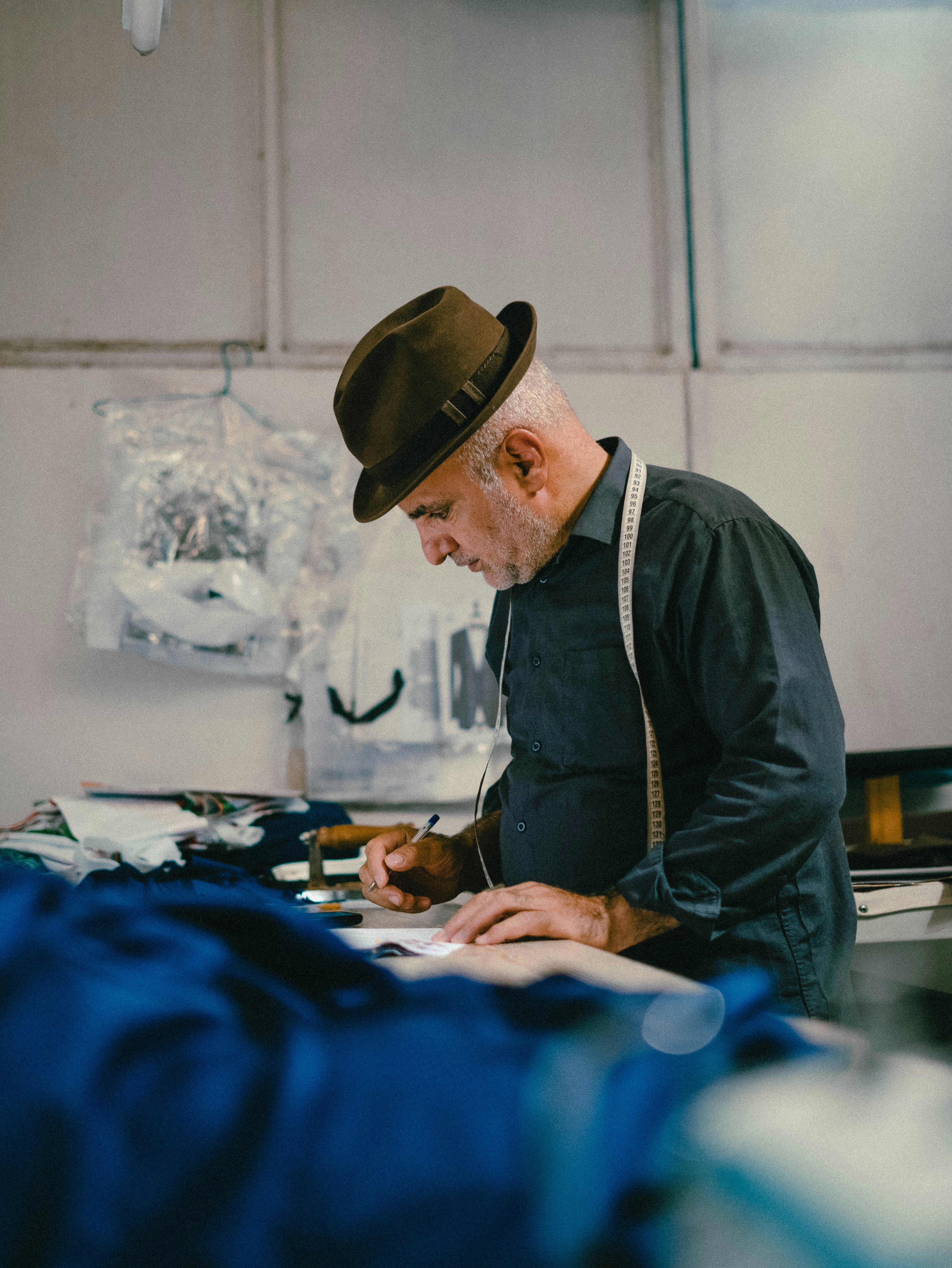A skilled tailor meticulously measures fabric while working at his sewing station, surrounded by tools of the trade and unfinished garments.