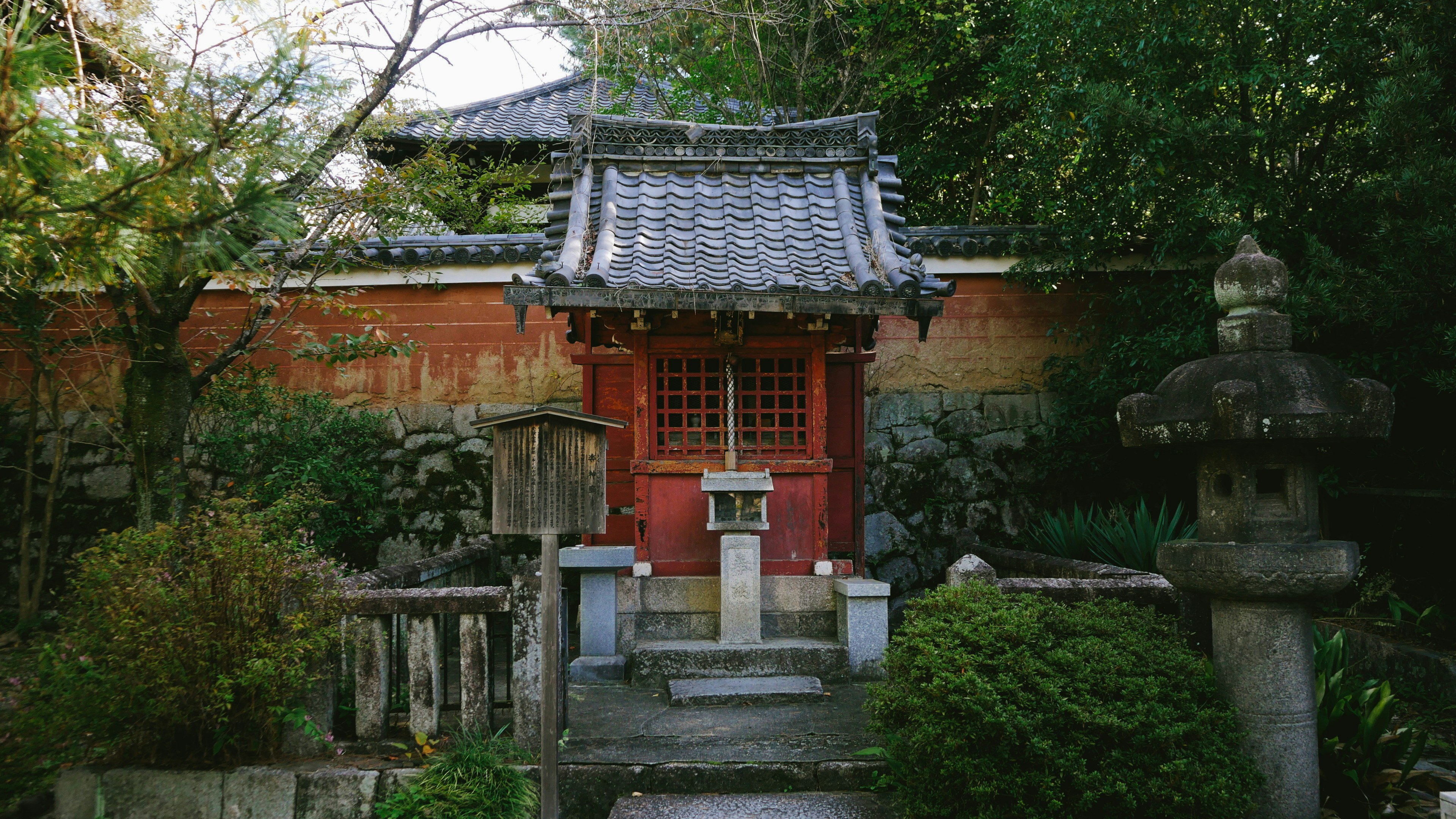 A small japanese shrine sits amidst greenery.