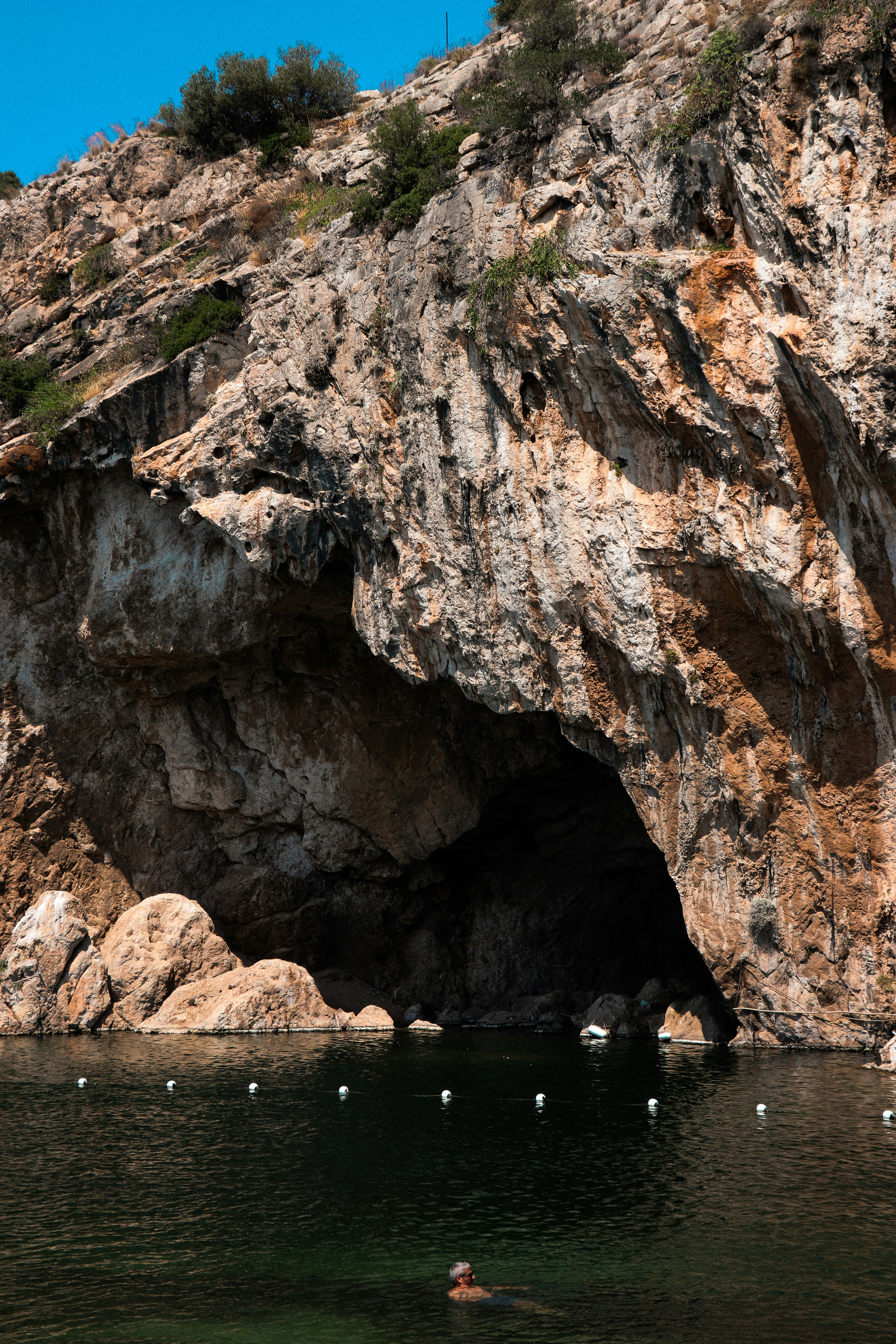 A dark cave opens above tranquil water.