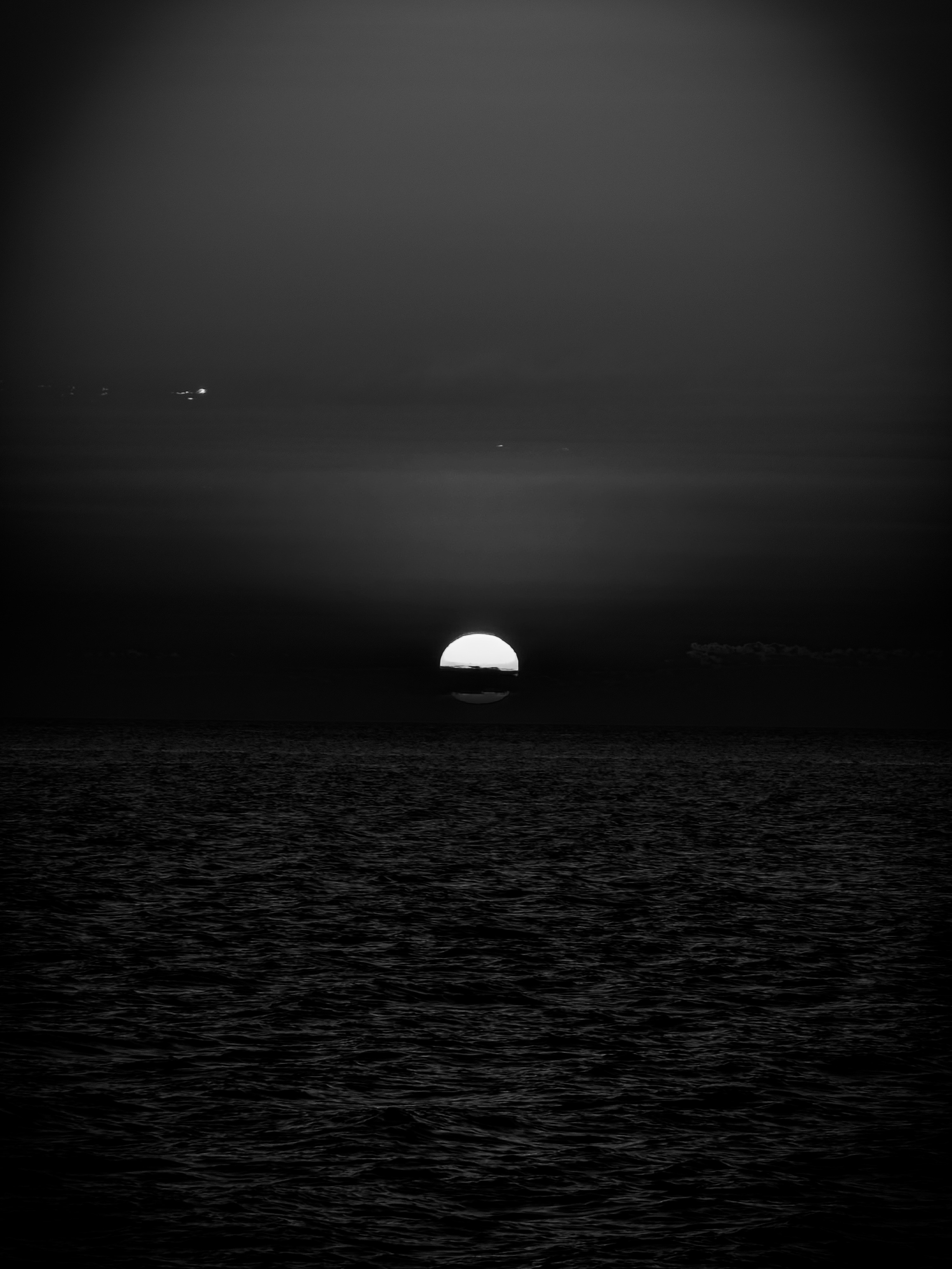 The sun sets over a dark, wavy ocean.