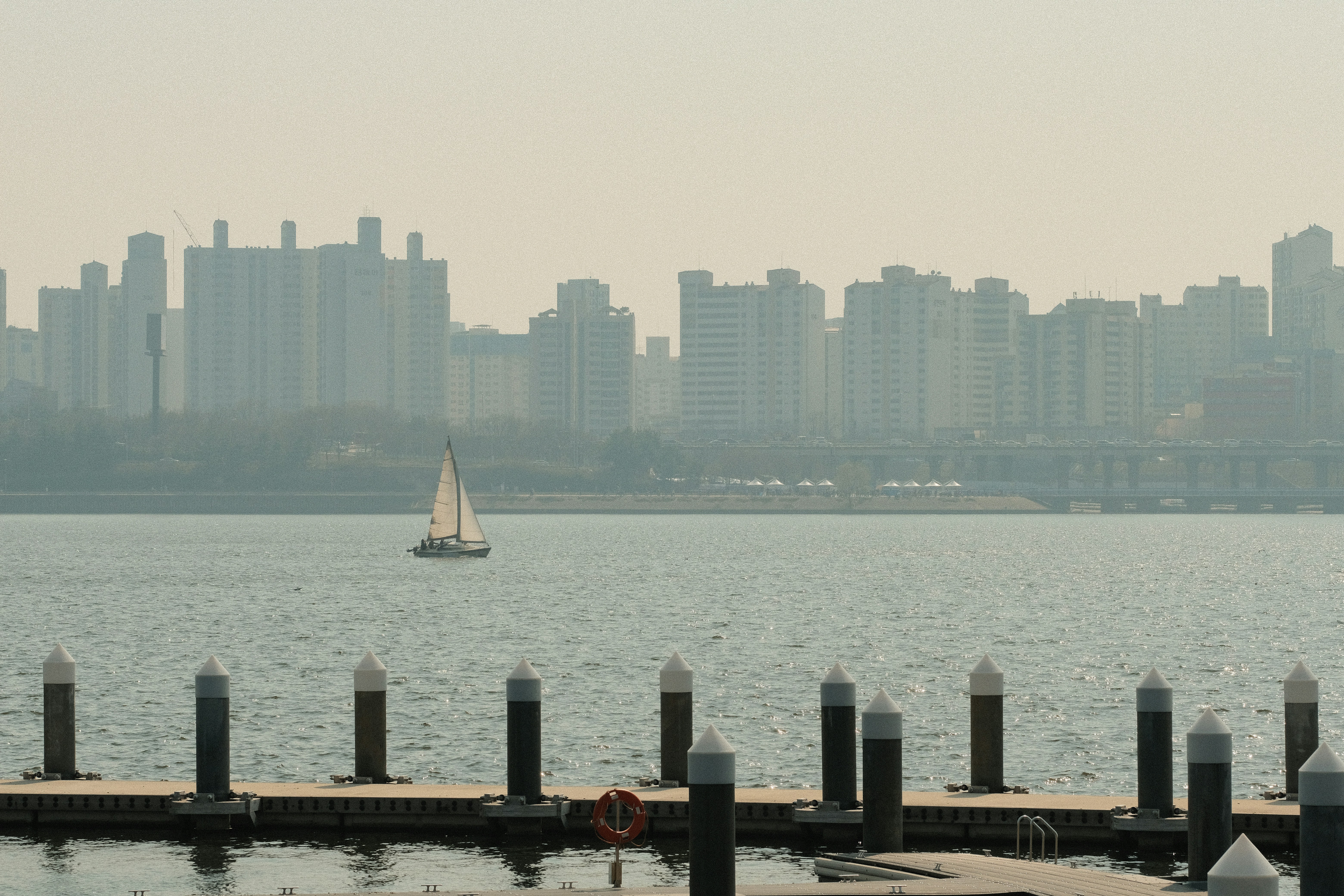 A sailboat glides across a calm, misty lake.