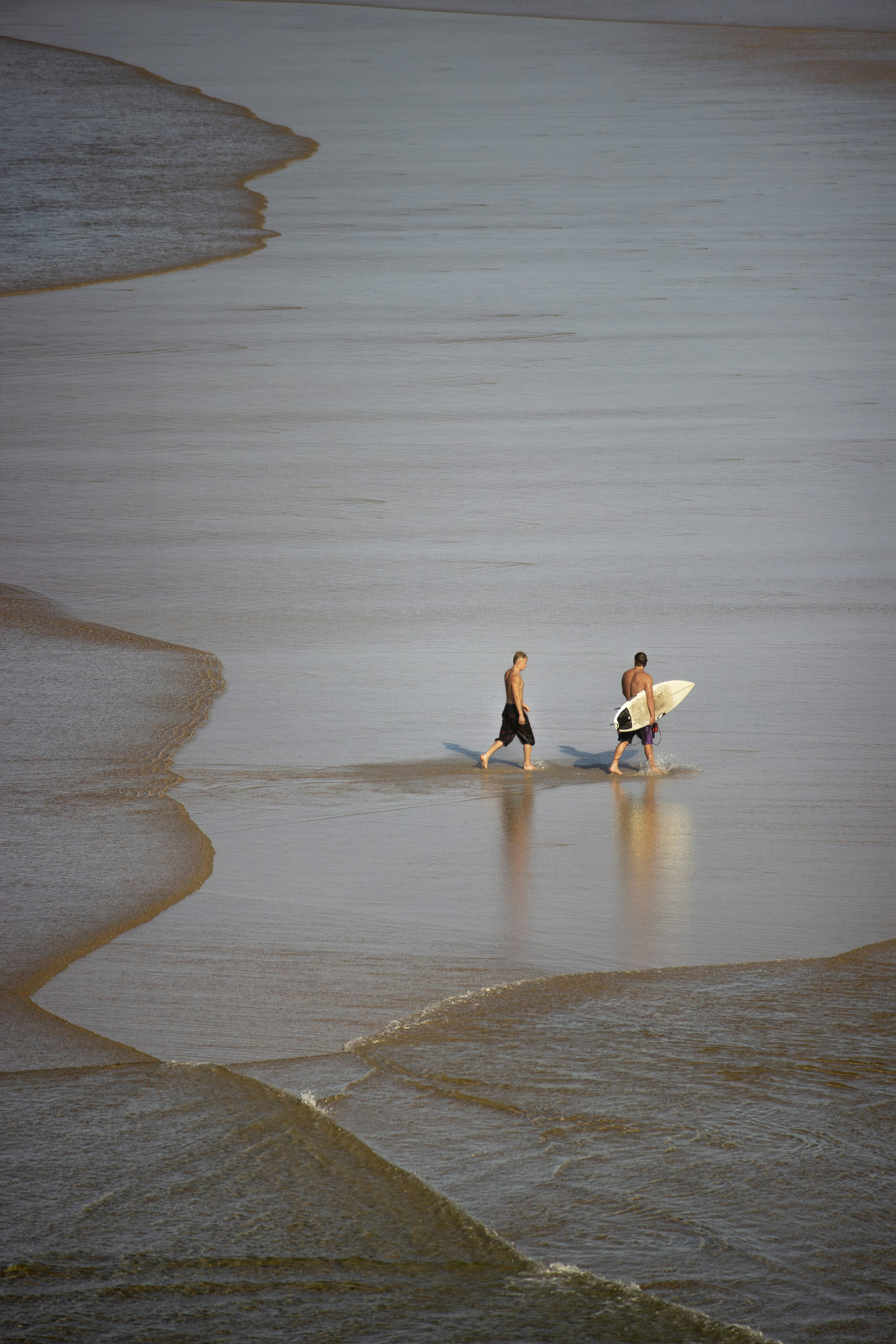 Surfers walk on the wet sand near the shore.
