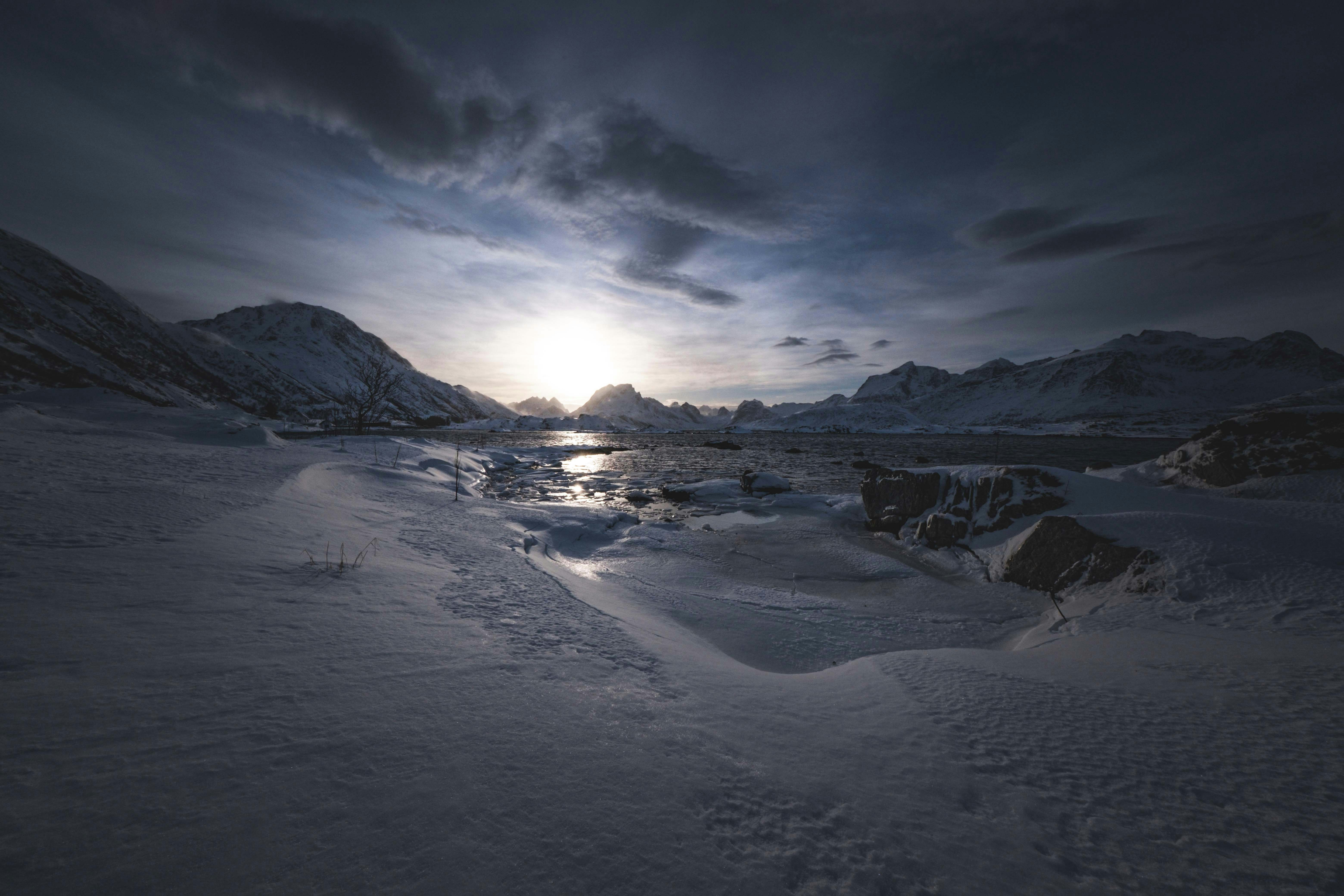 A serene winter landscape featuring snow-covered mountains and a reflective body of water under a moody sky.