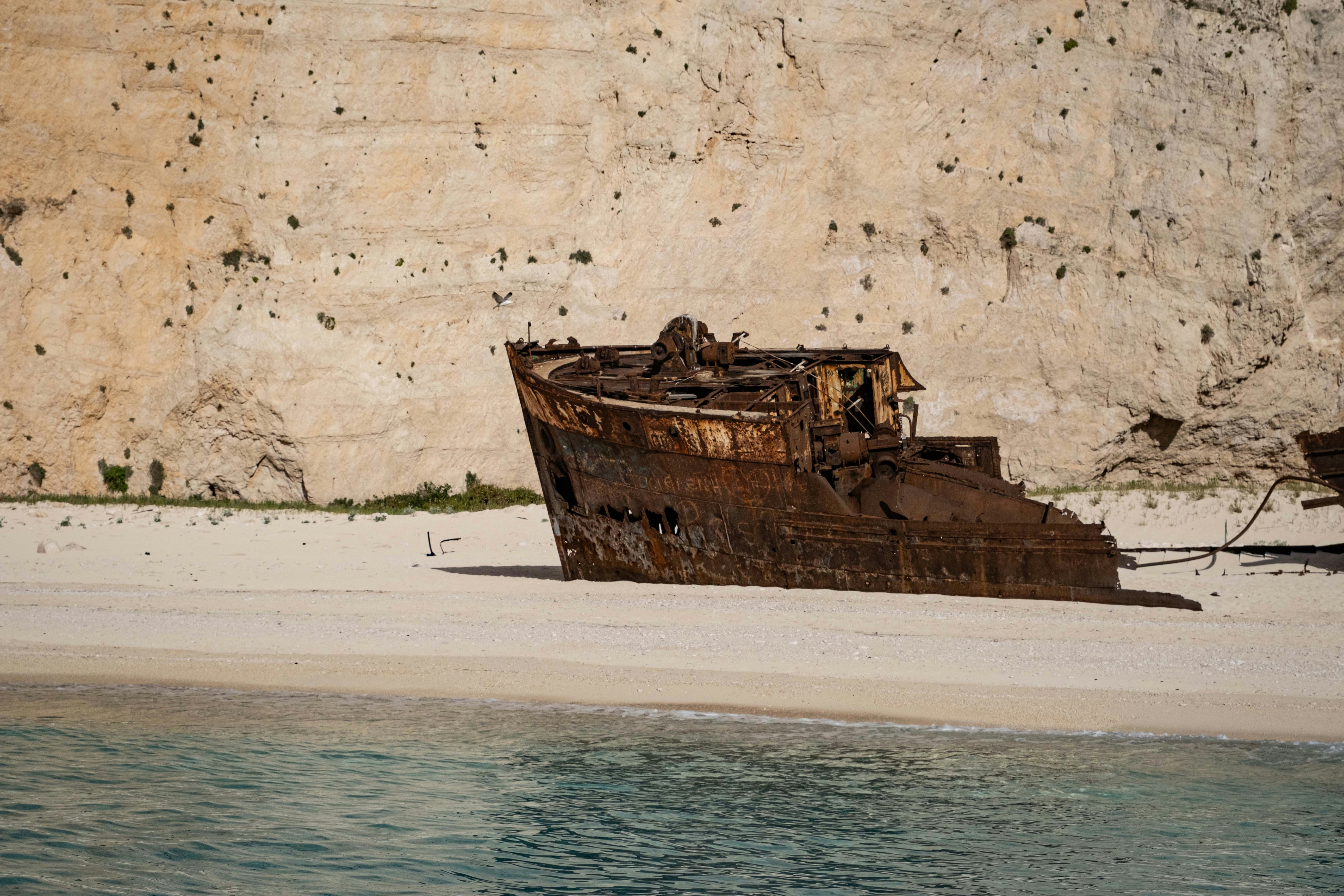 A rusted shipwreck rests on a sandy beach.