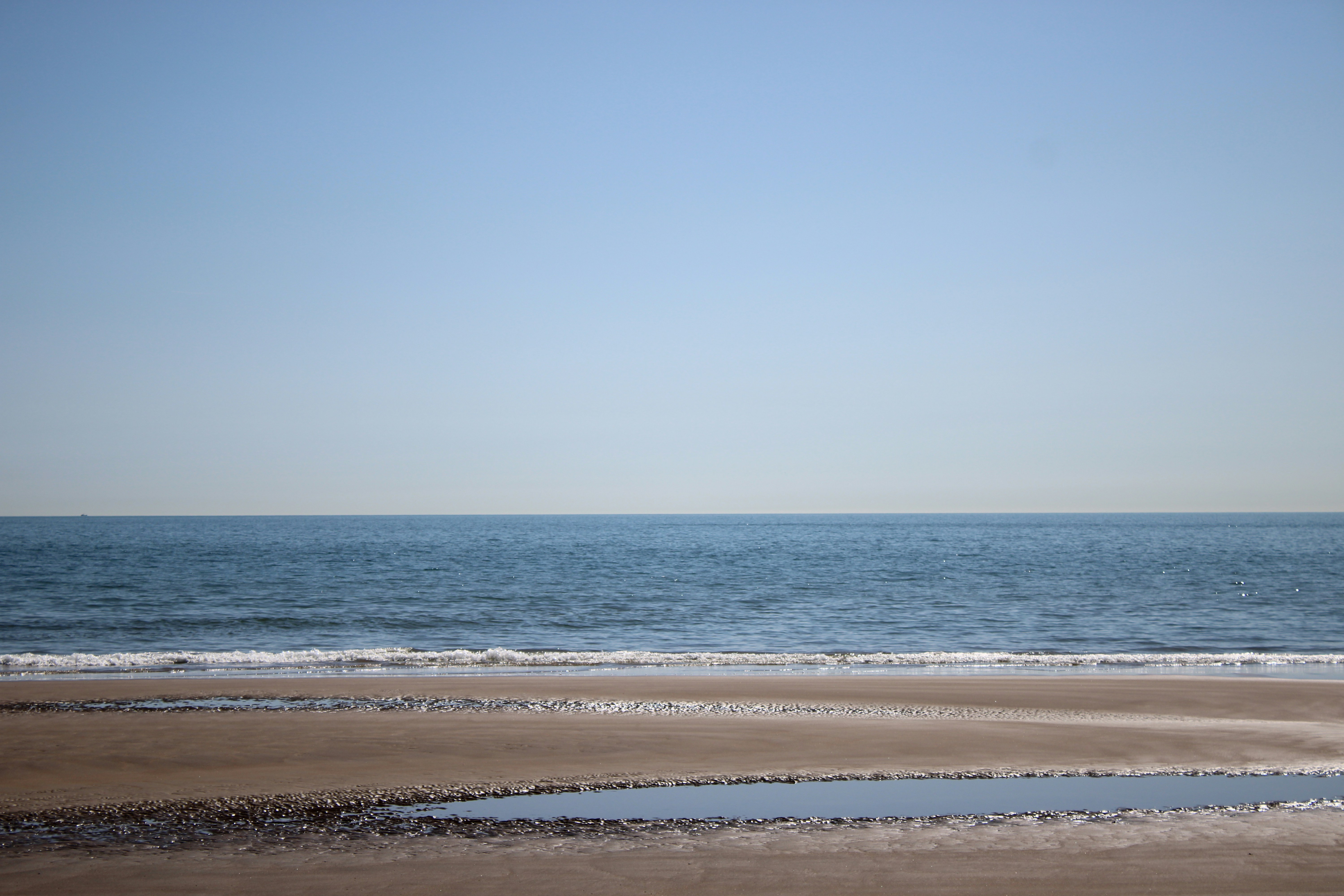 Sandy beach, blue calm ocean, and colourful clear skies | Beach, sea, and sky create a tranquil scene.