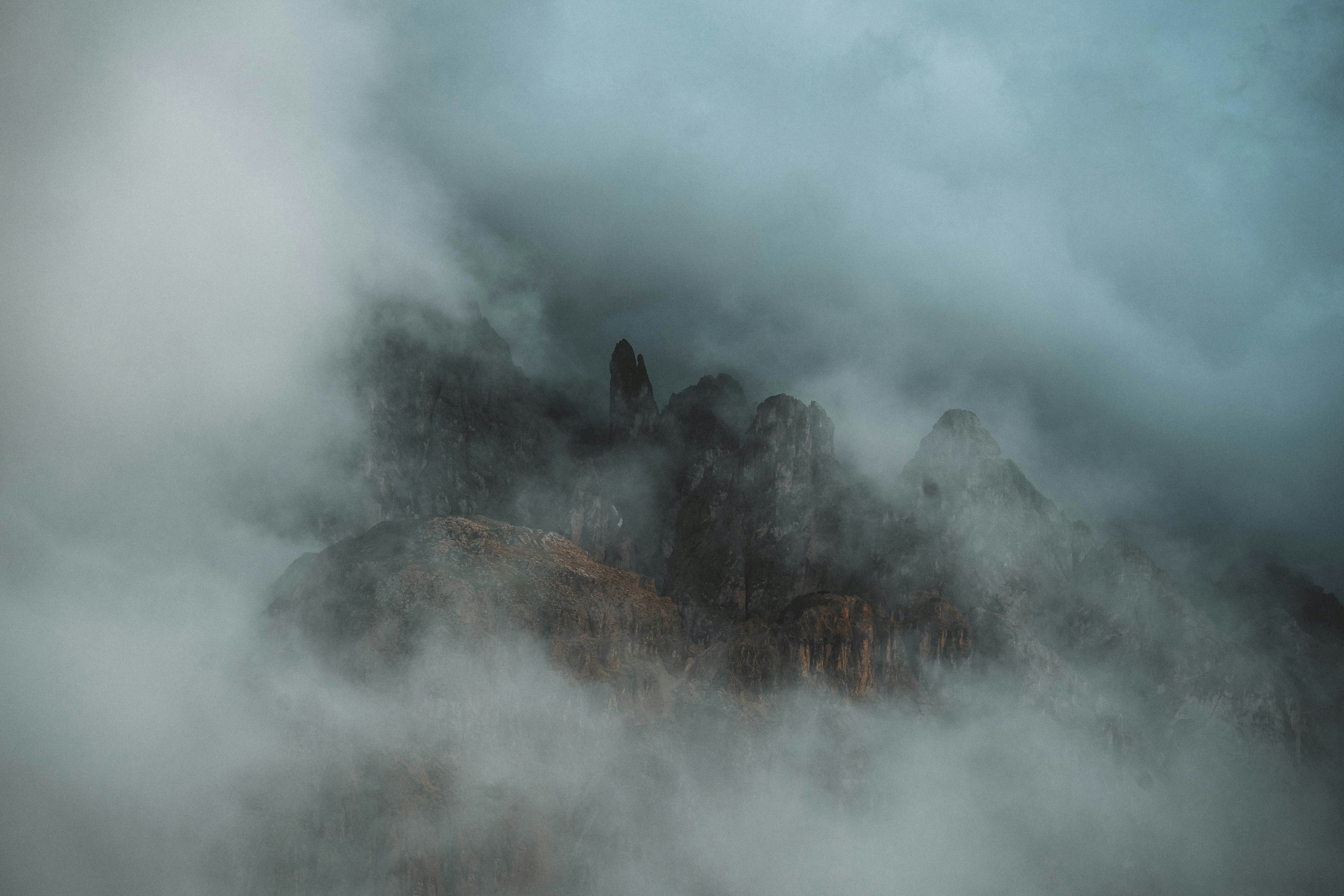 Majestic mountain peaks partially obscured by swirling clouds, creating an ethereal landscape. The interplay of light and shadow adds depth to the rugged terrain.