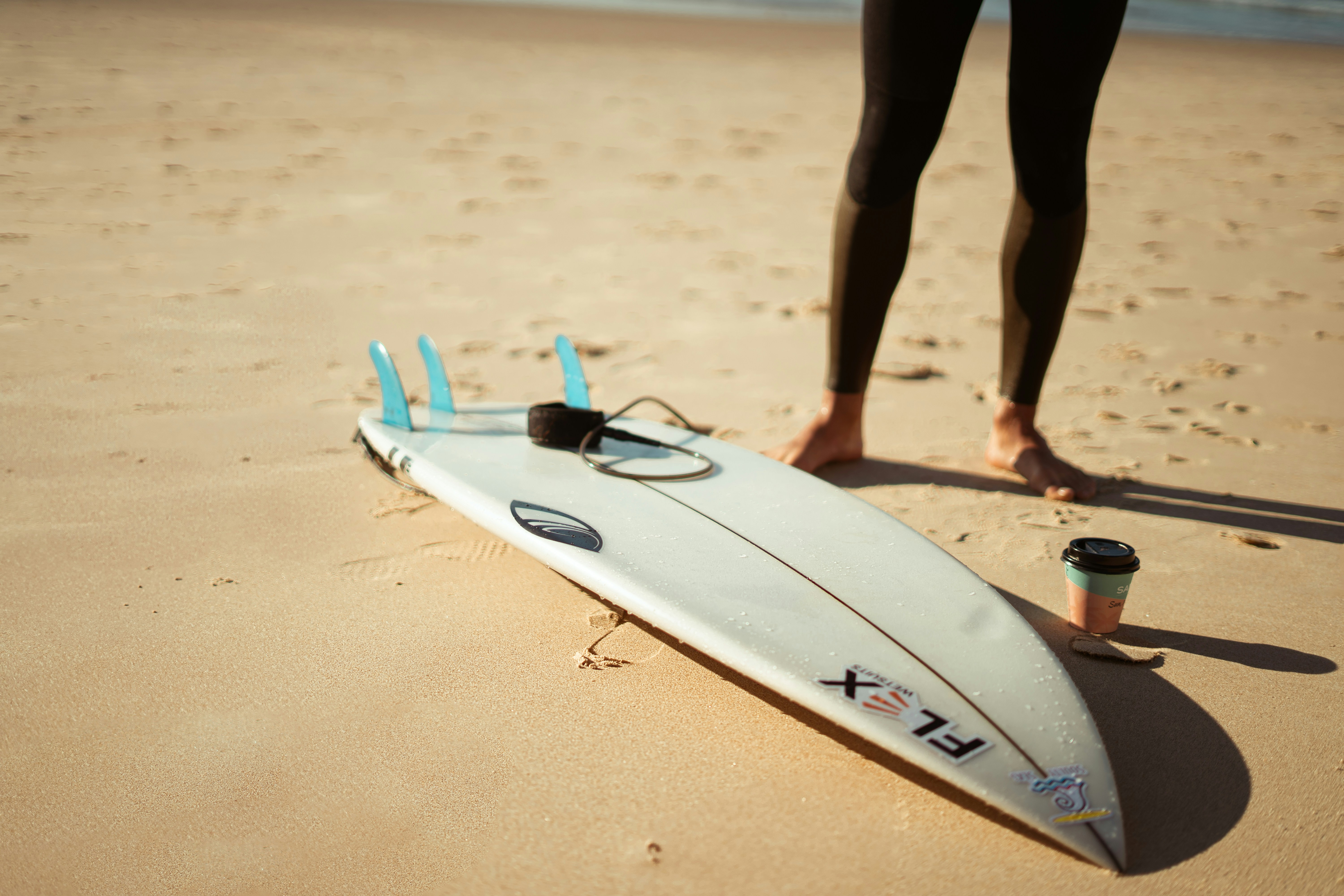 Surfer stands near surfboard on sandy beach.