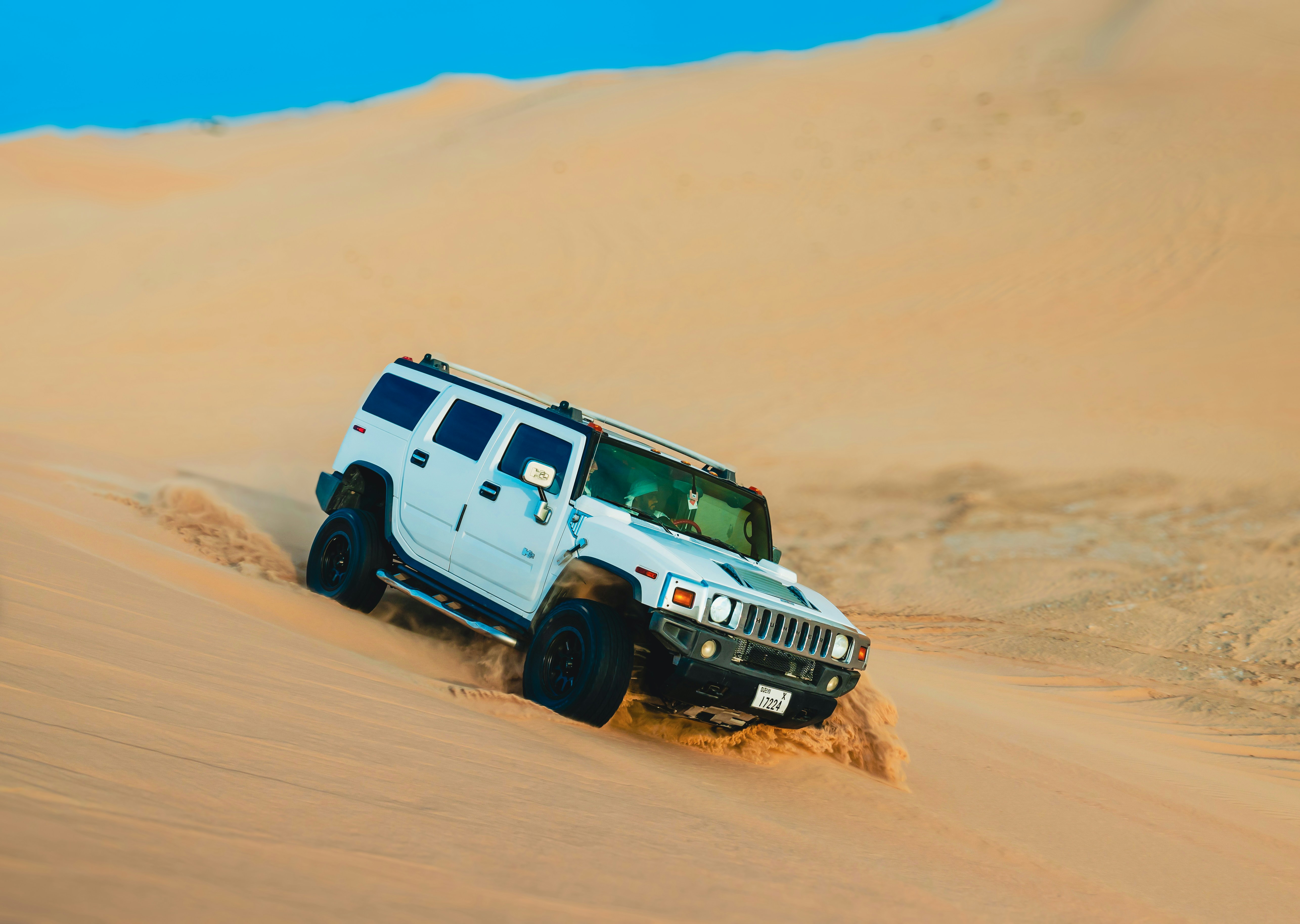 A white Hummer navigating the sandy dunes, showcasing its off-road capabilities against a clear blue sky.