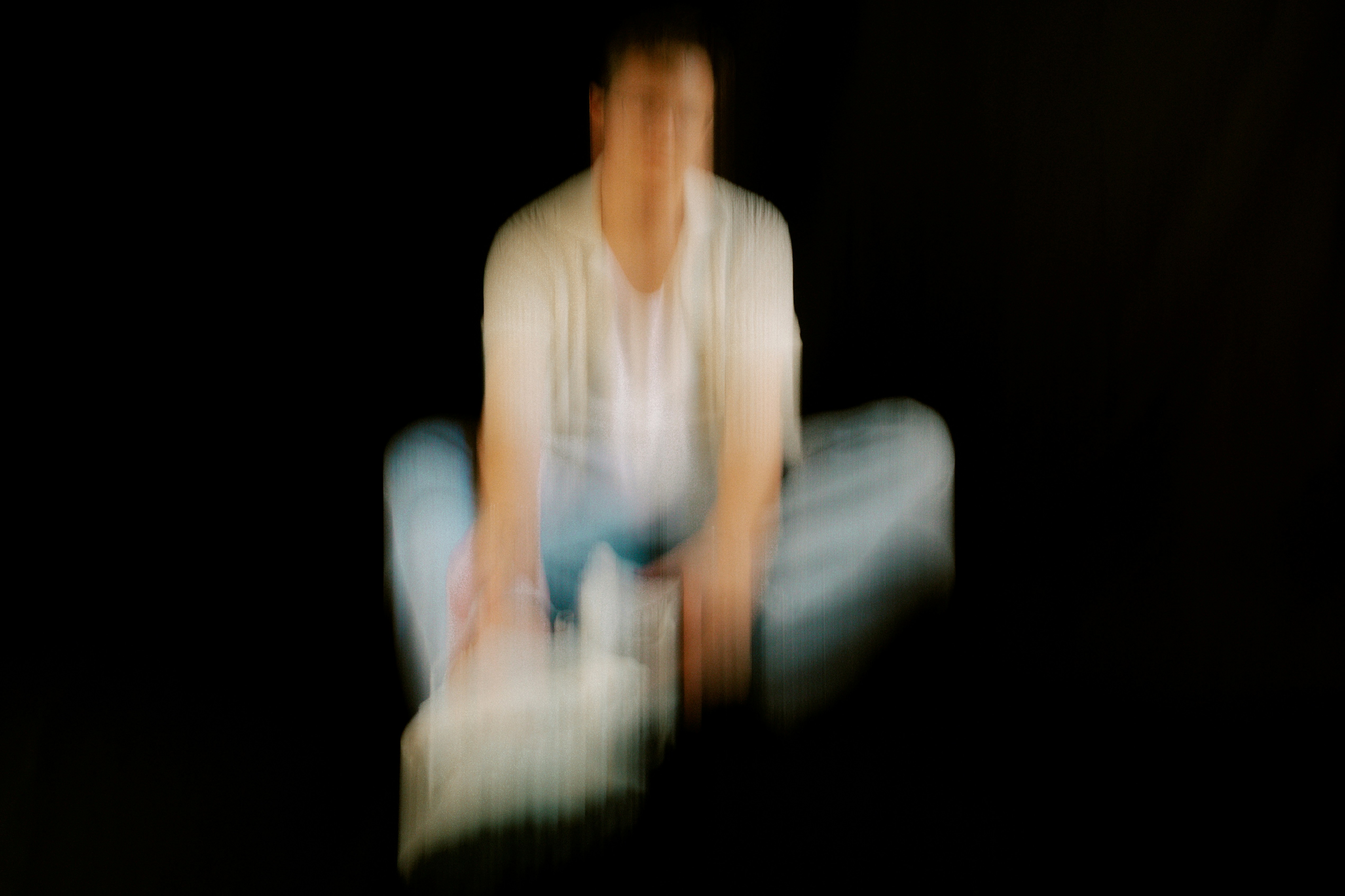 A blurred person is sitting in a dark space.