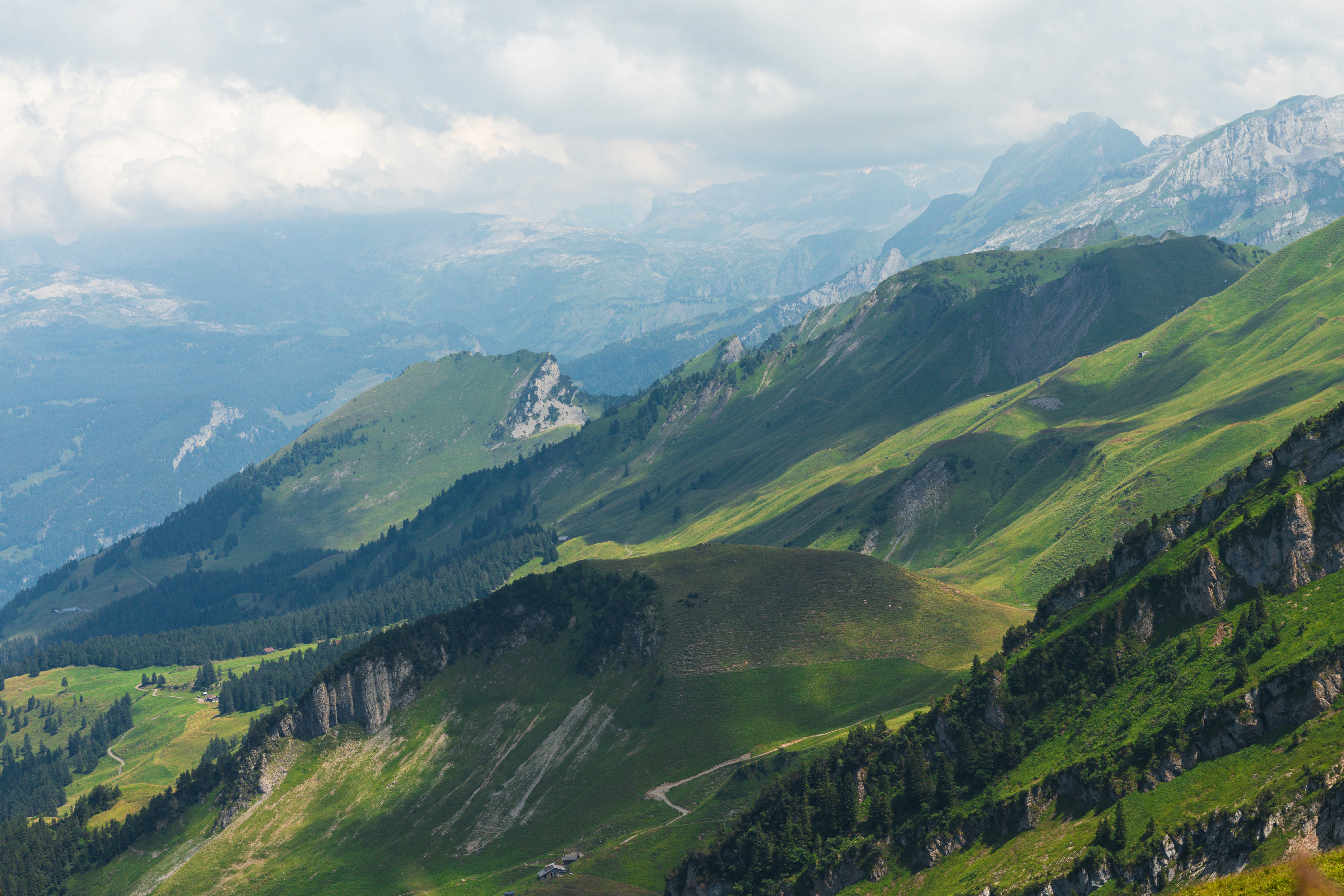 Lush green mountains undulate under a moody sky, showcasing the dynamic interplay of light and shadow across the landscape.