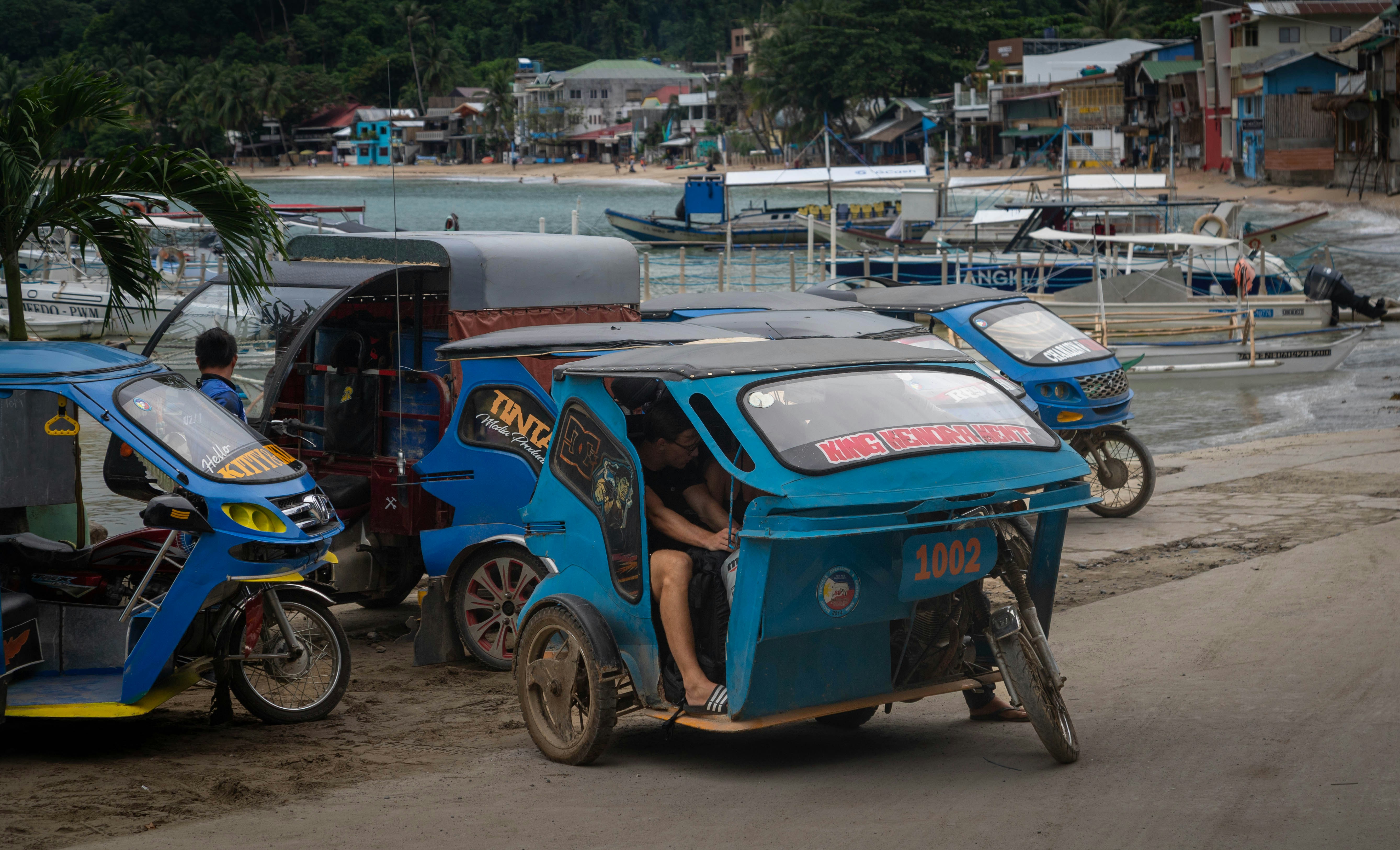 Tricycles are parked near a beach in a town.