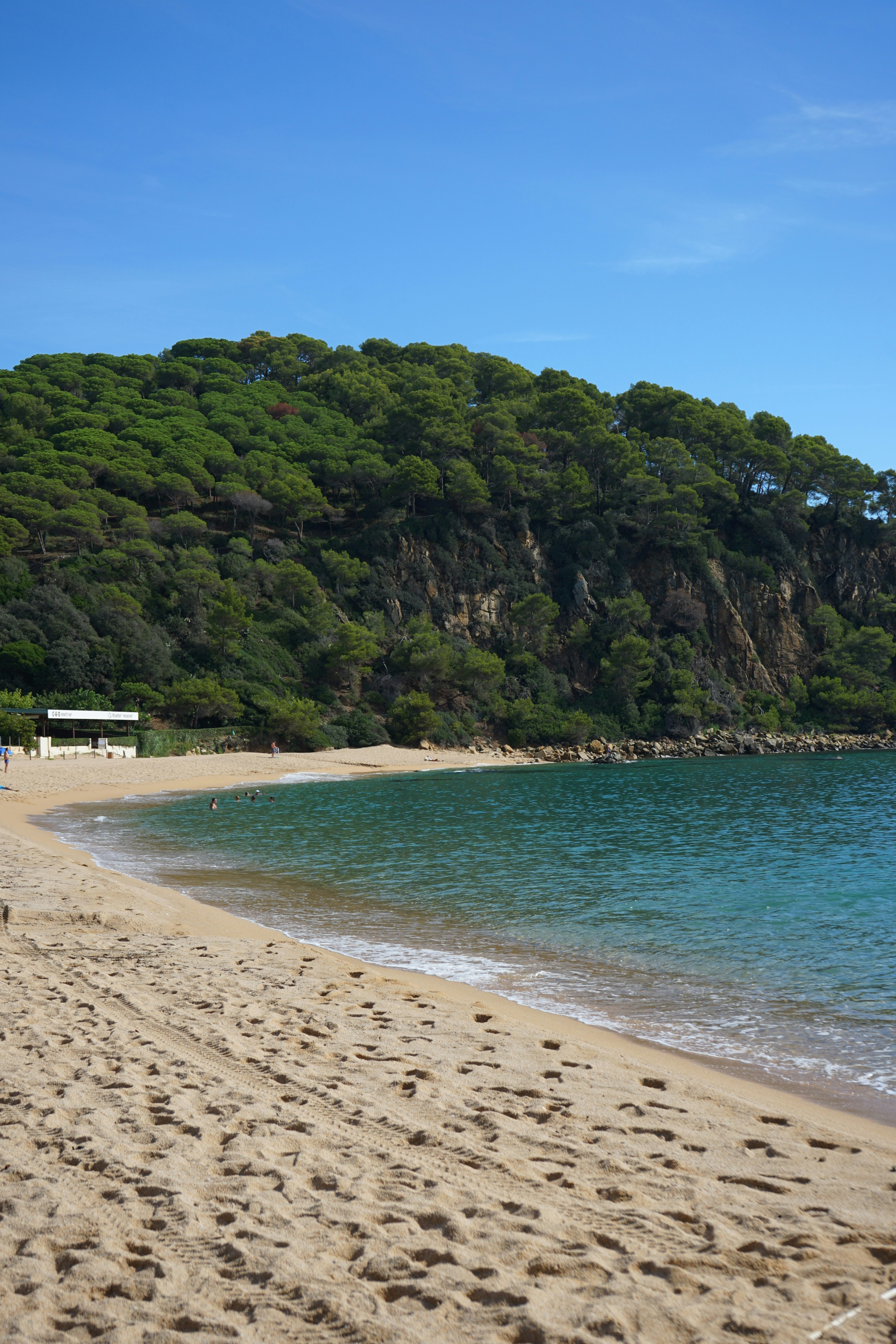 Tranquil beach scene with soft golden sand and clear turquoise waters, framed by lush greenery and rocky cliffs in the background.