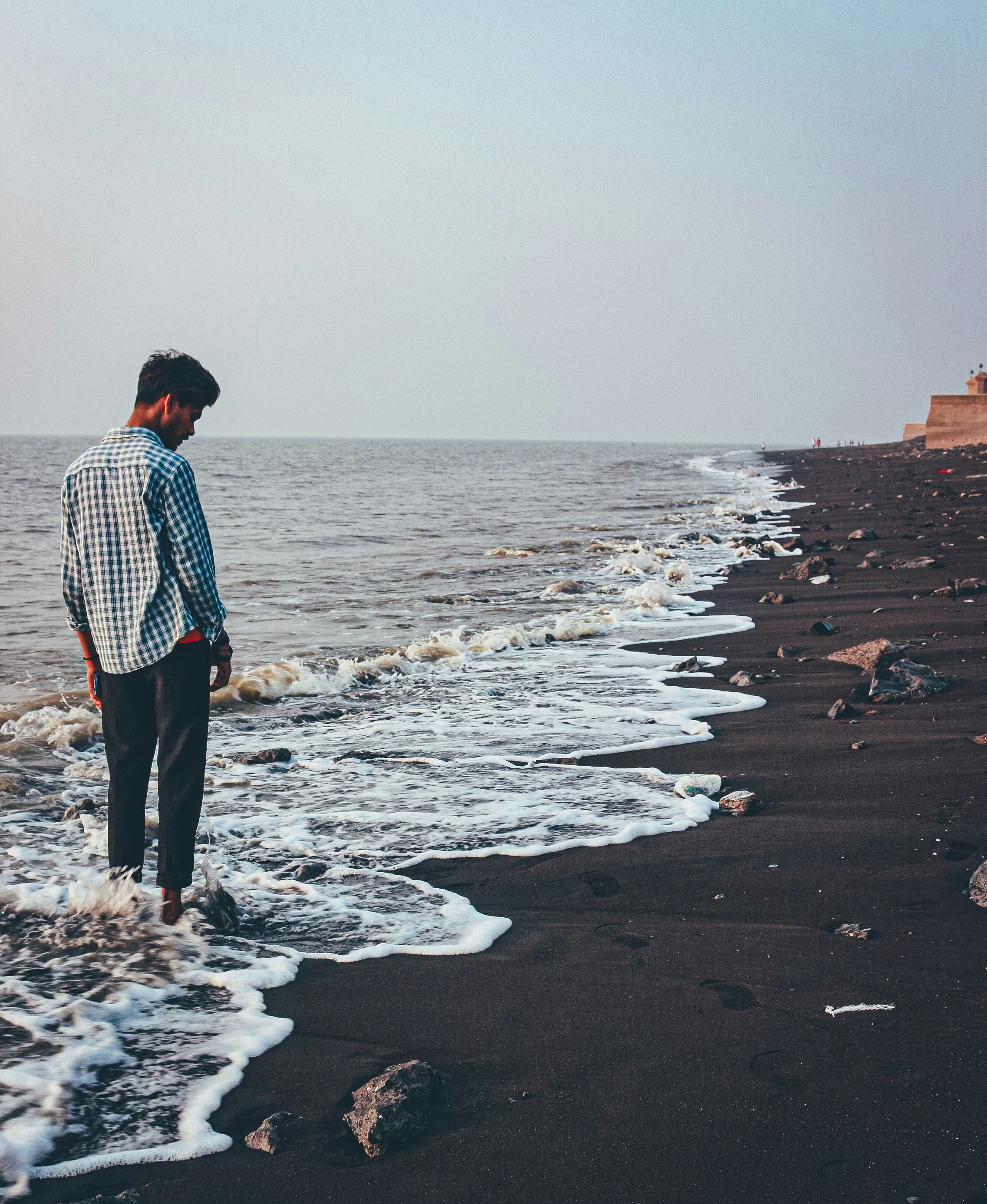 Man standing beach side | A man stands in the waves on a beach.