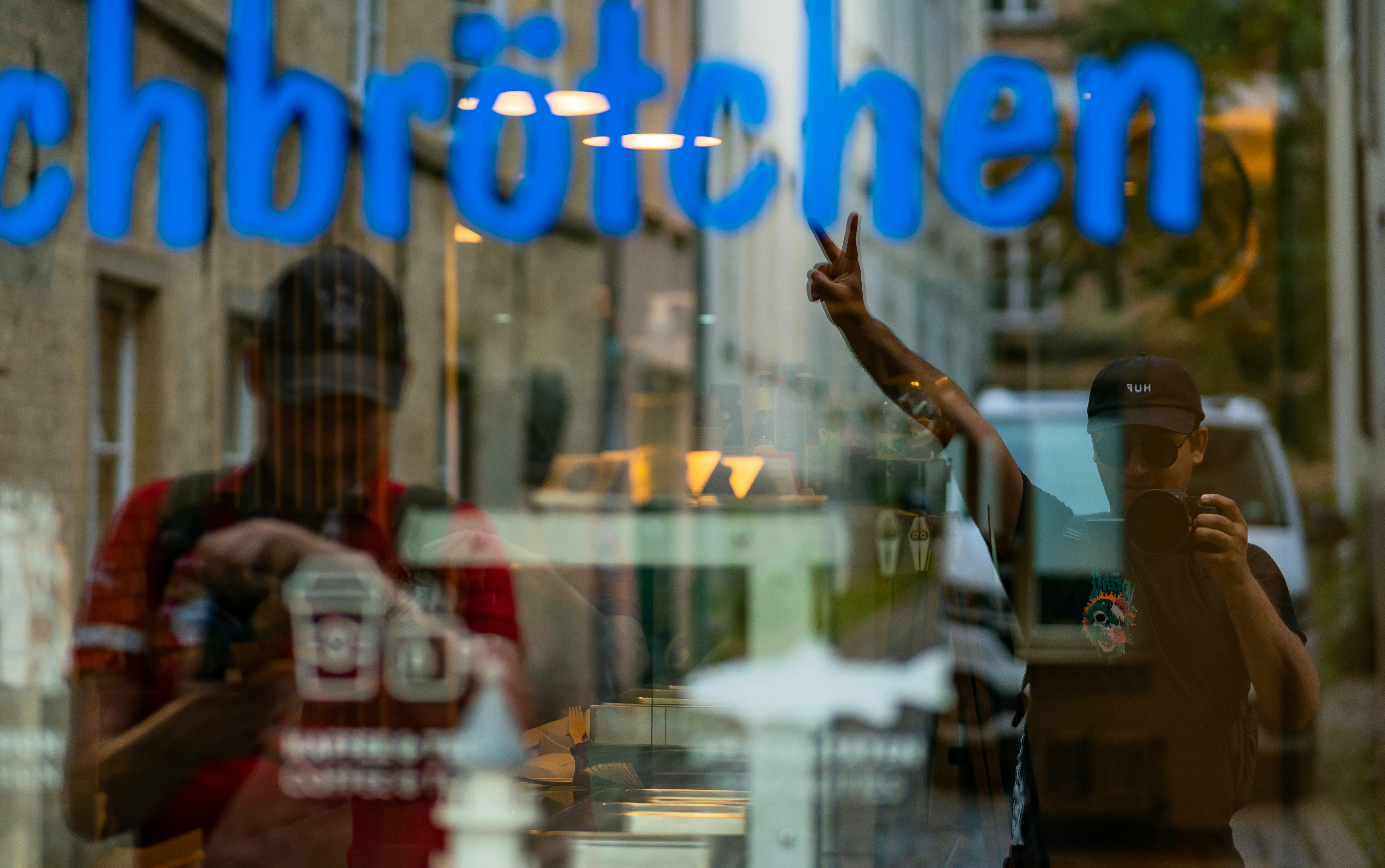 People are reflected in a window, one giving a peace sign.