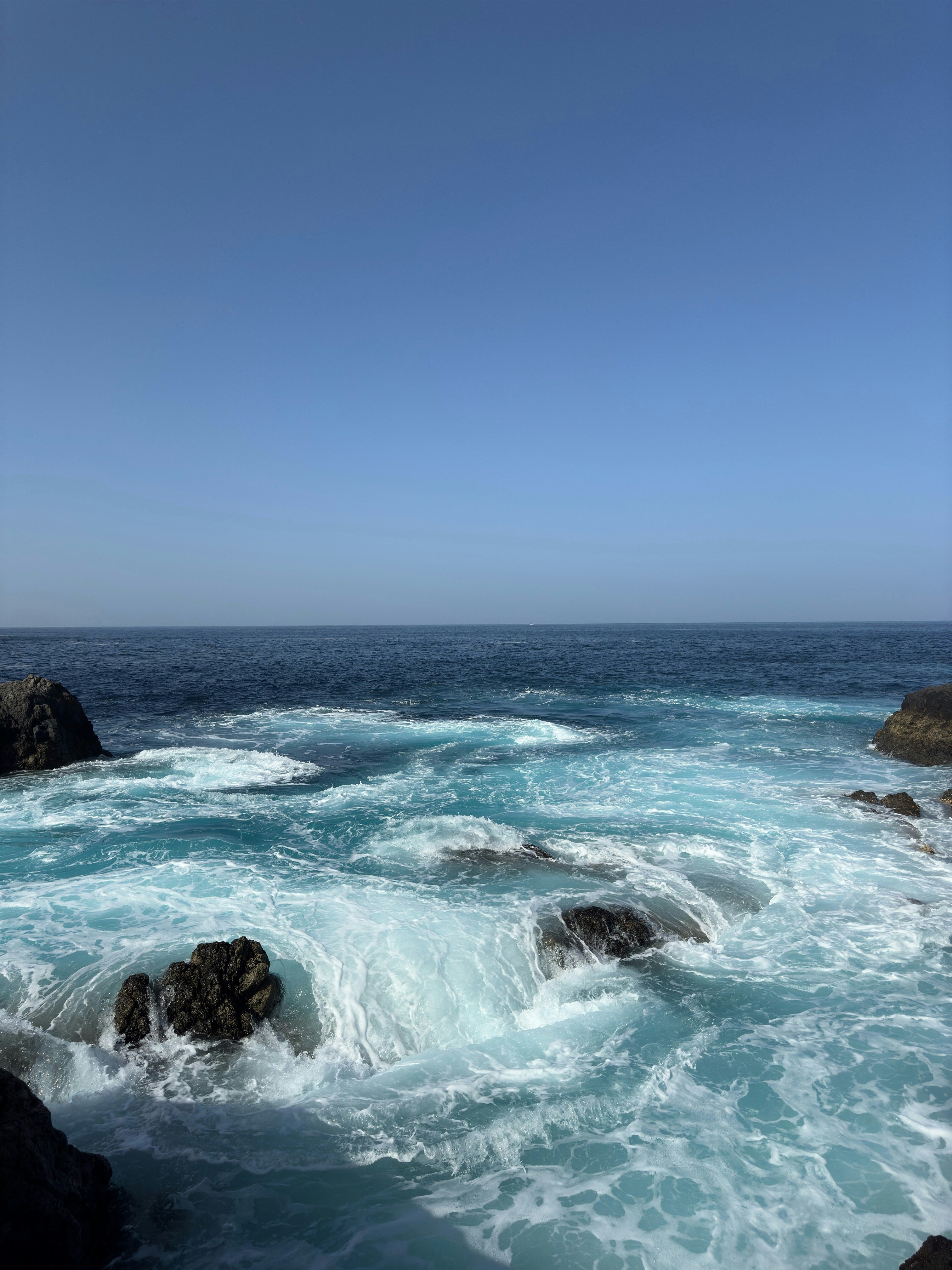 https://www.instagram.com/paria_world7 | Waves crash against rocks under a clear blue sky.