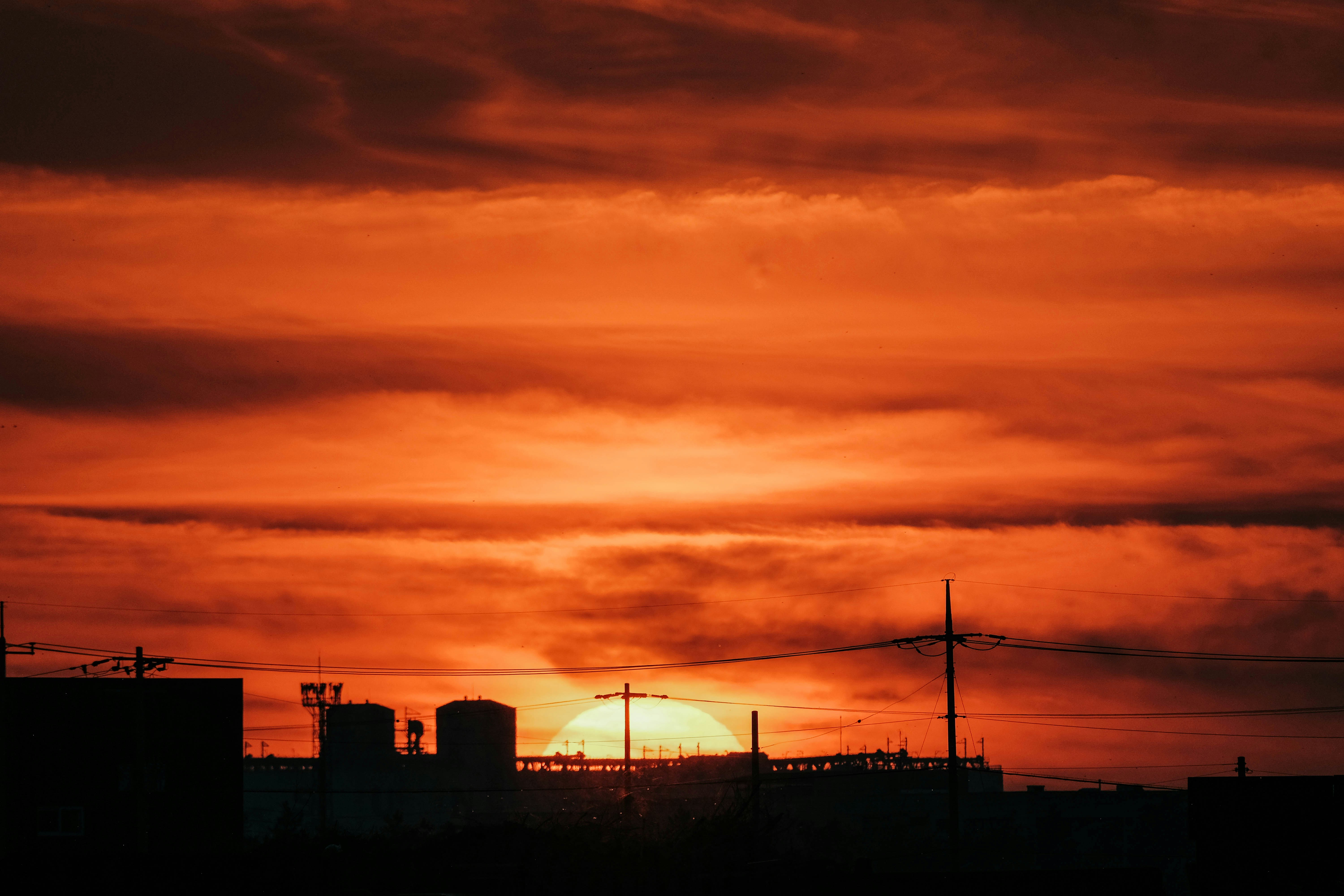 Silhouetted industrial skyline against a vibrant sunset, with the sun dipping below the horizon. The scene captures the interplay of light and shadow.