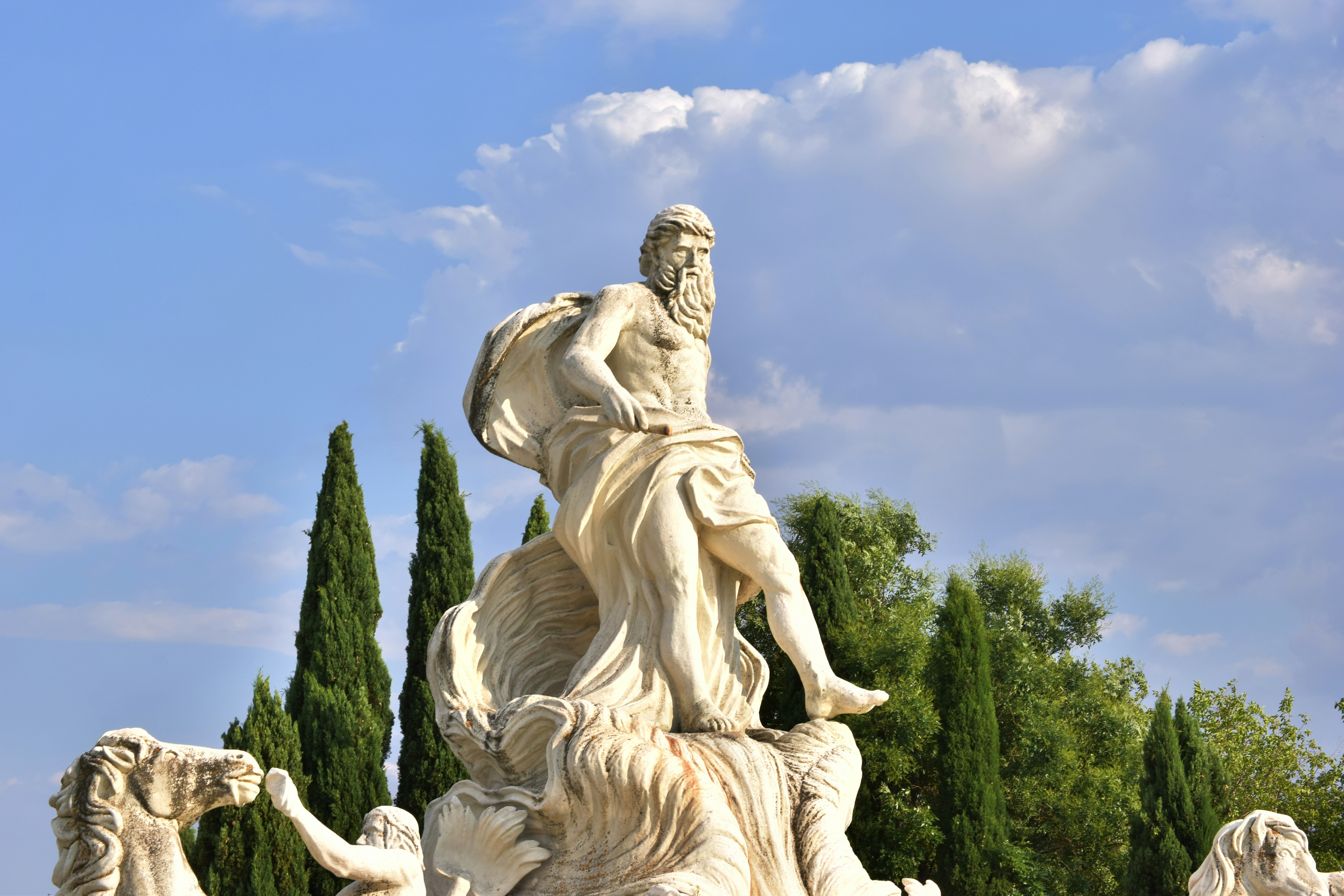 A classical statue stands before a cloudy sky.