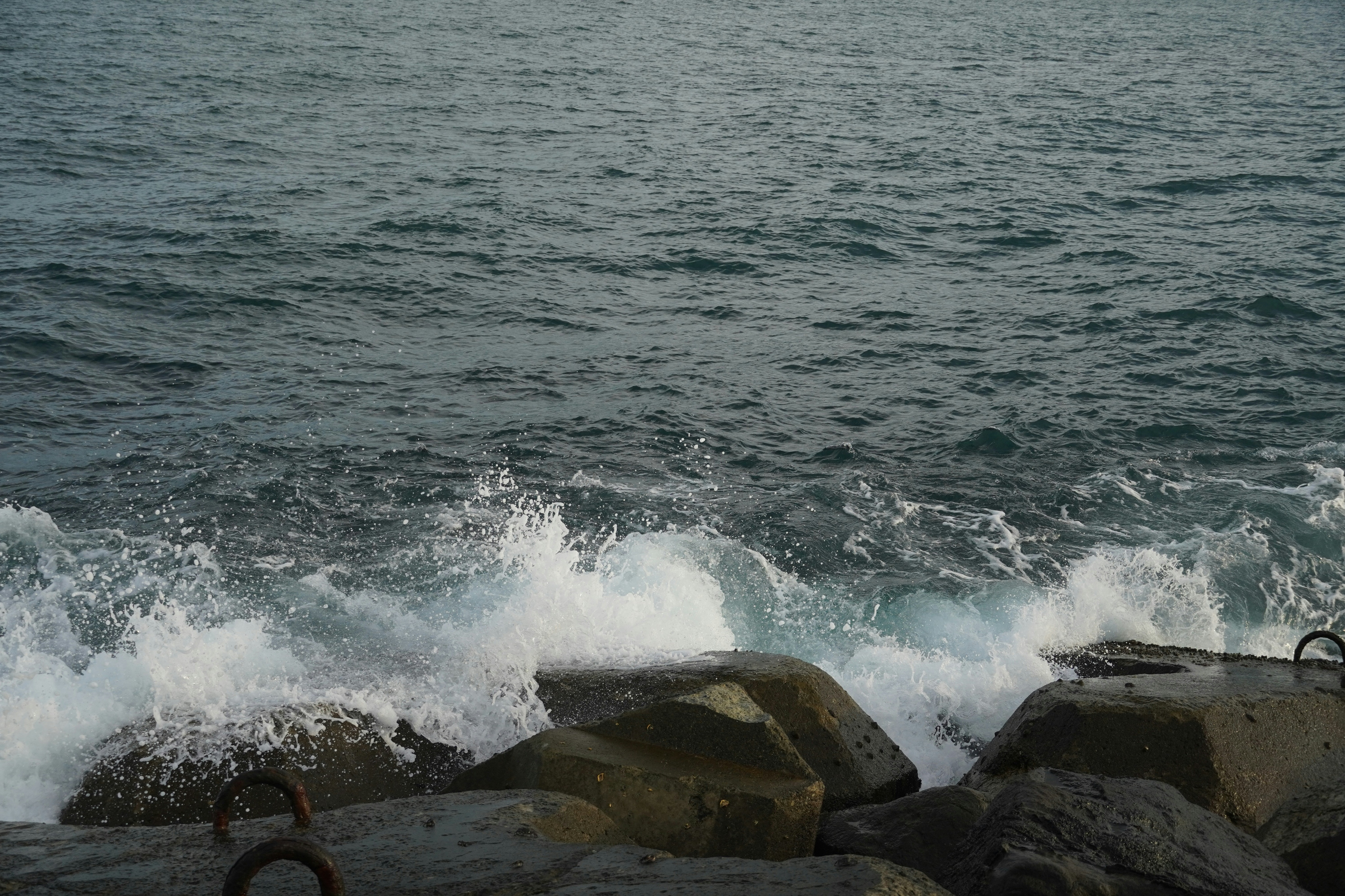 Foamy waves crashing against rugged rocks along a coastal shoreline, capturing the dynamic interplay of water and stone.