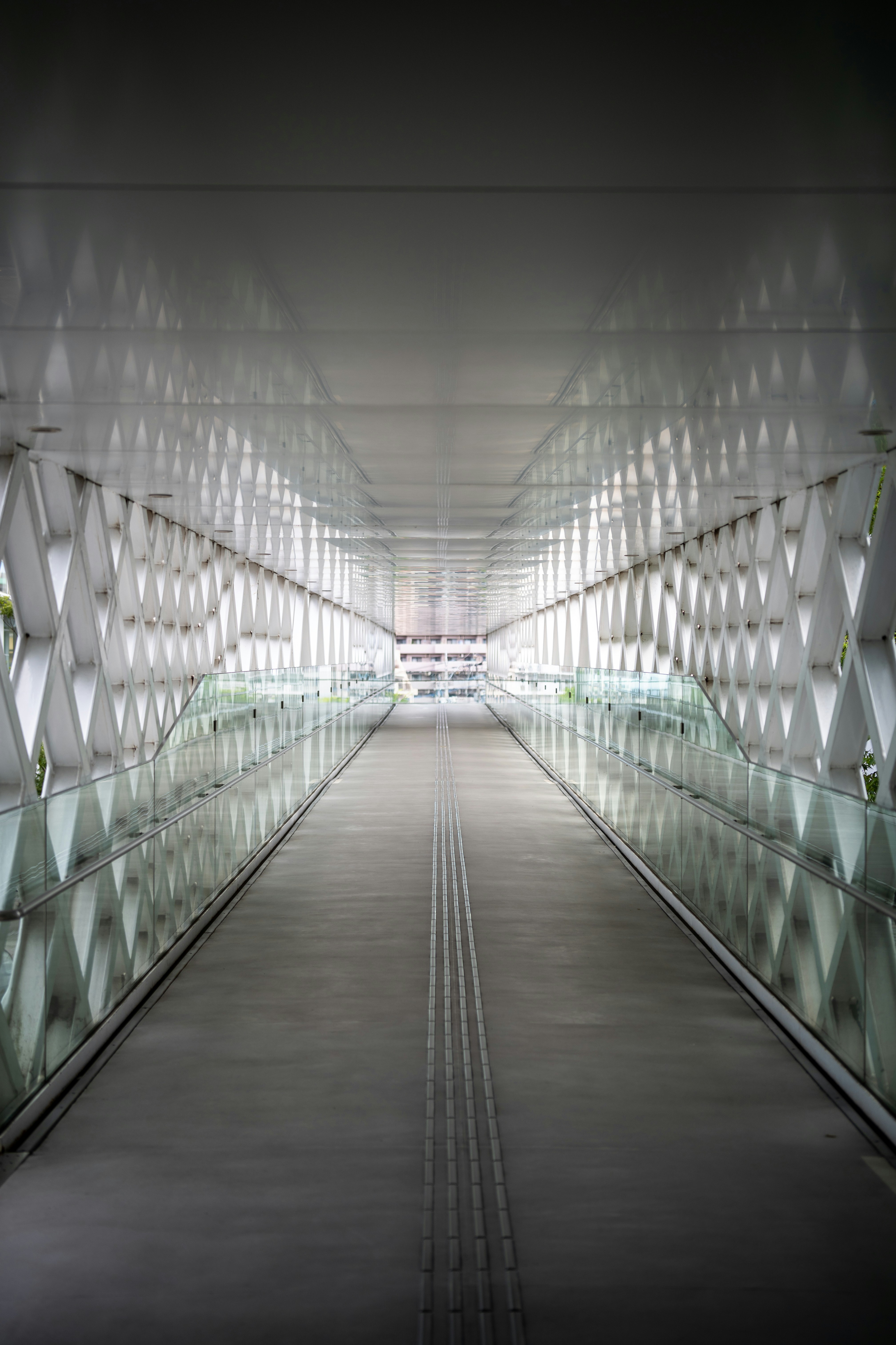 A sleek, contemporary walkway featuring reflective glass and geometric patterns, leading towards a bright exit. The design emphasizes symmetry and light.