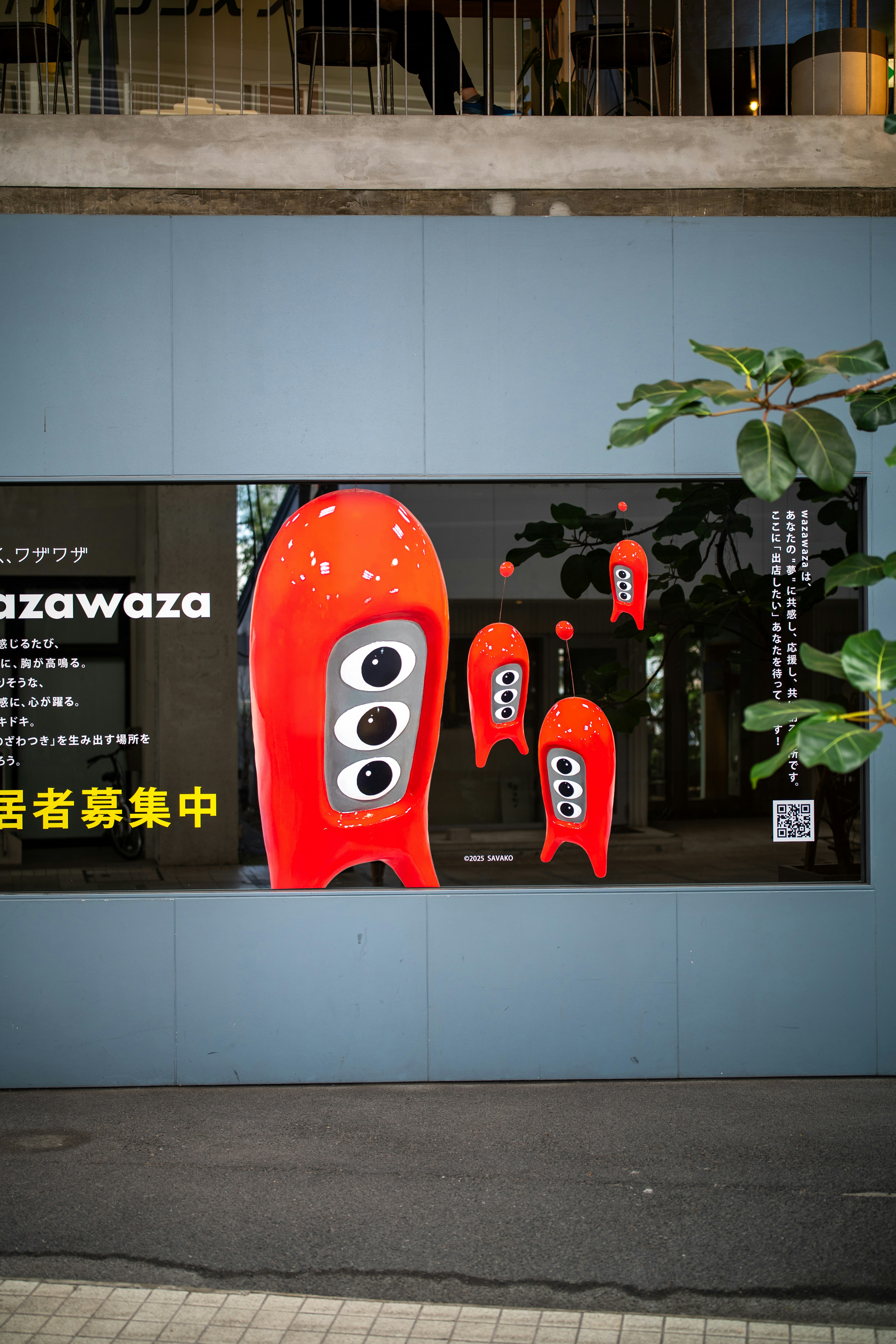 Vibrant red characters with large eyes featured prominently in a storefront display, inviting passersby to engage. The design combines playful elements with a modern aesthetic.