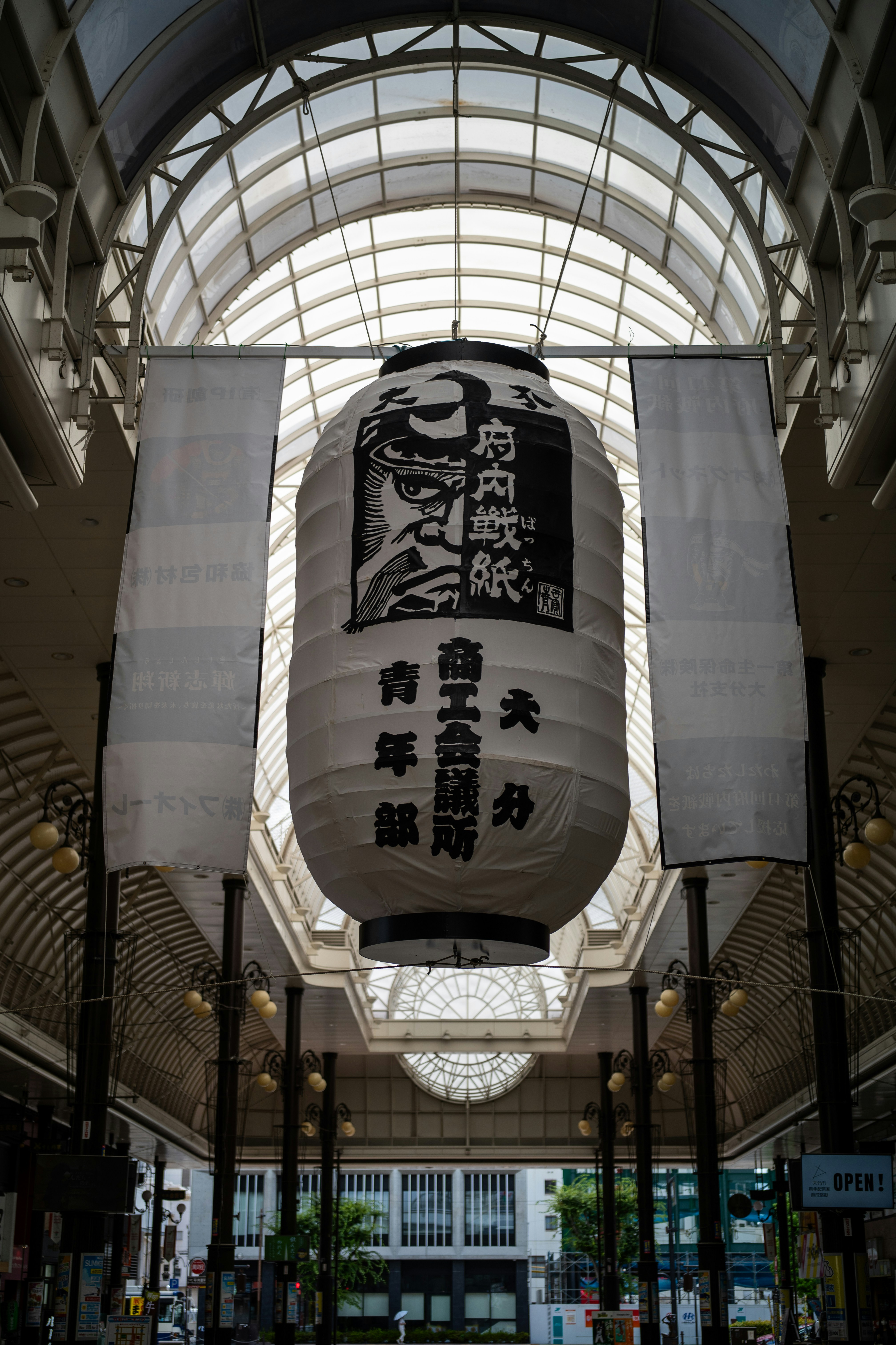 Traditional Japanese lantern featuring a detailed face design, suspended in a bustling indoor market space with a glass ceiling.