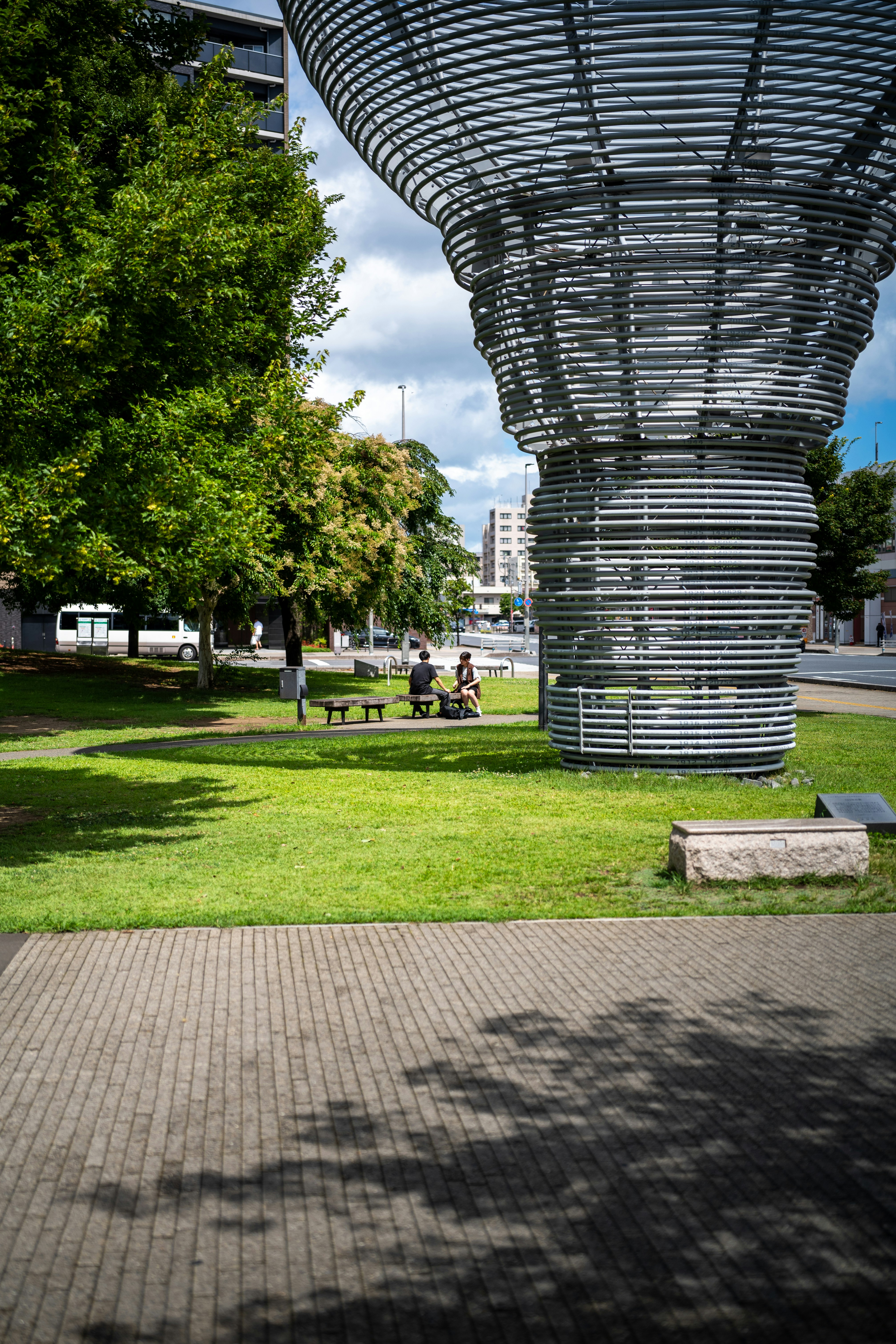 People sit in a park near an art installation.