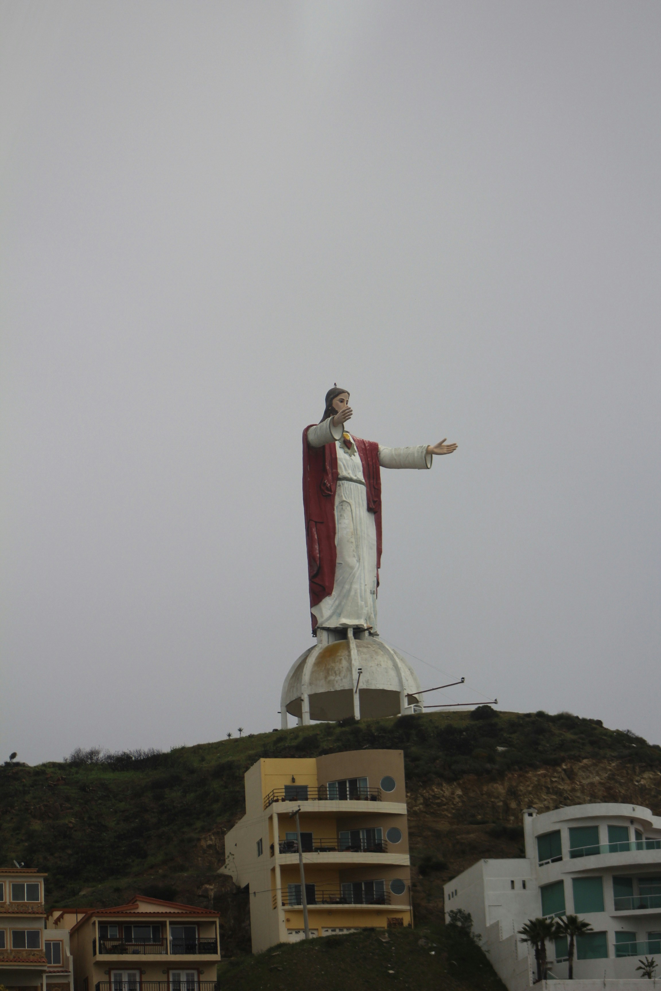 Statue of jesus stands atop a small mountain.