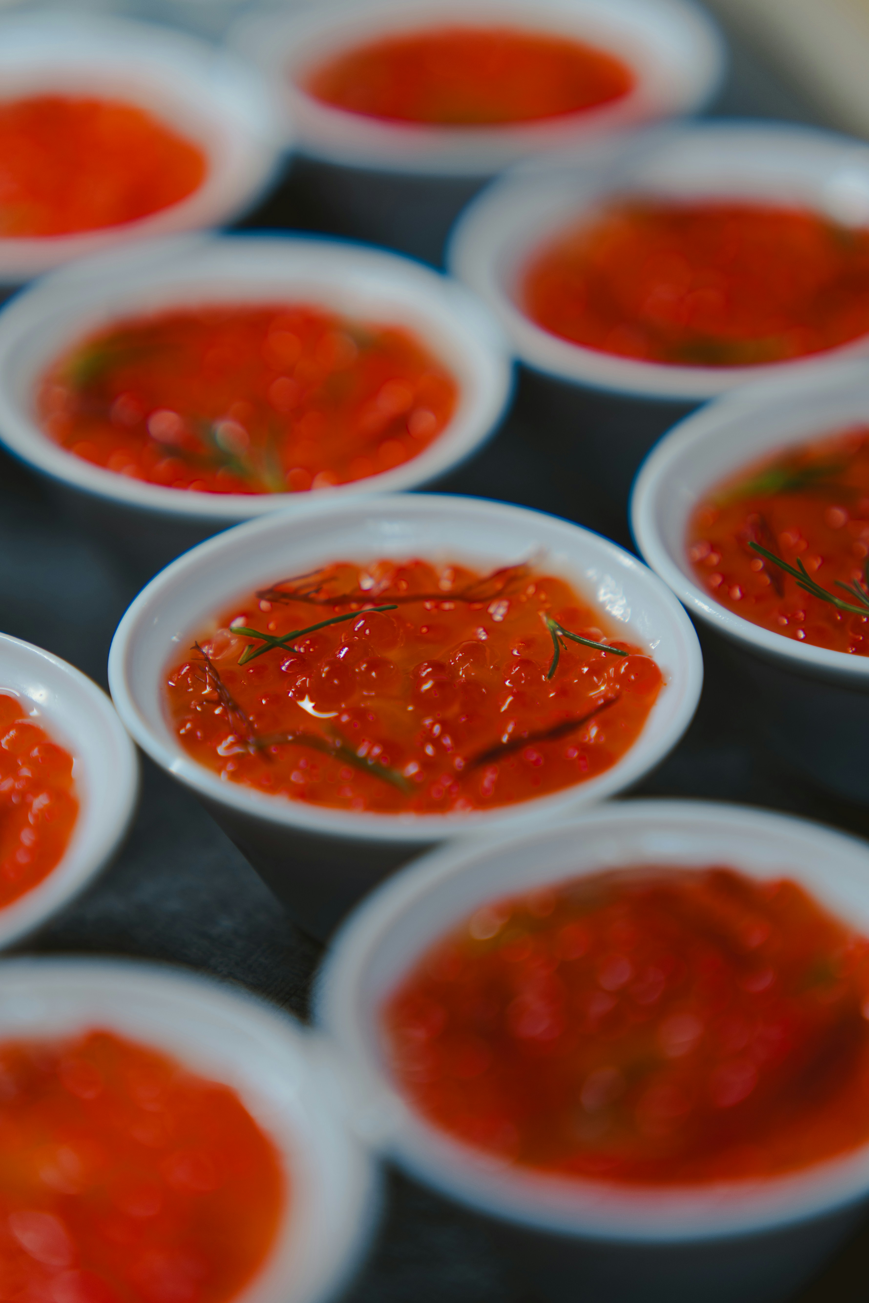 Small white bowls filled with vibrant salmon roe, garnished with fresh herbs, arranged elegantly on a dark surface.