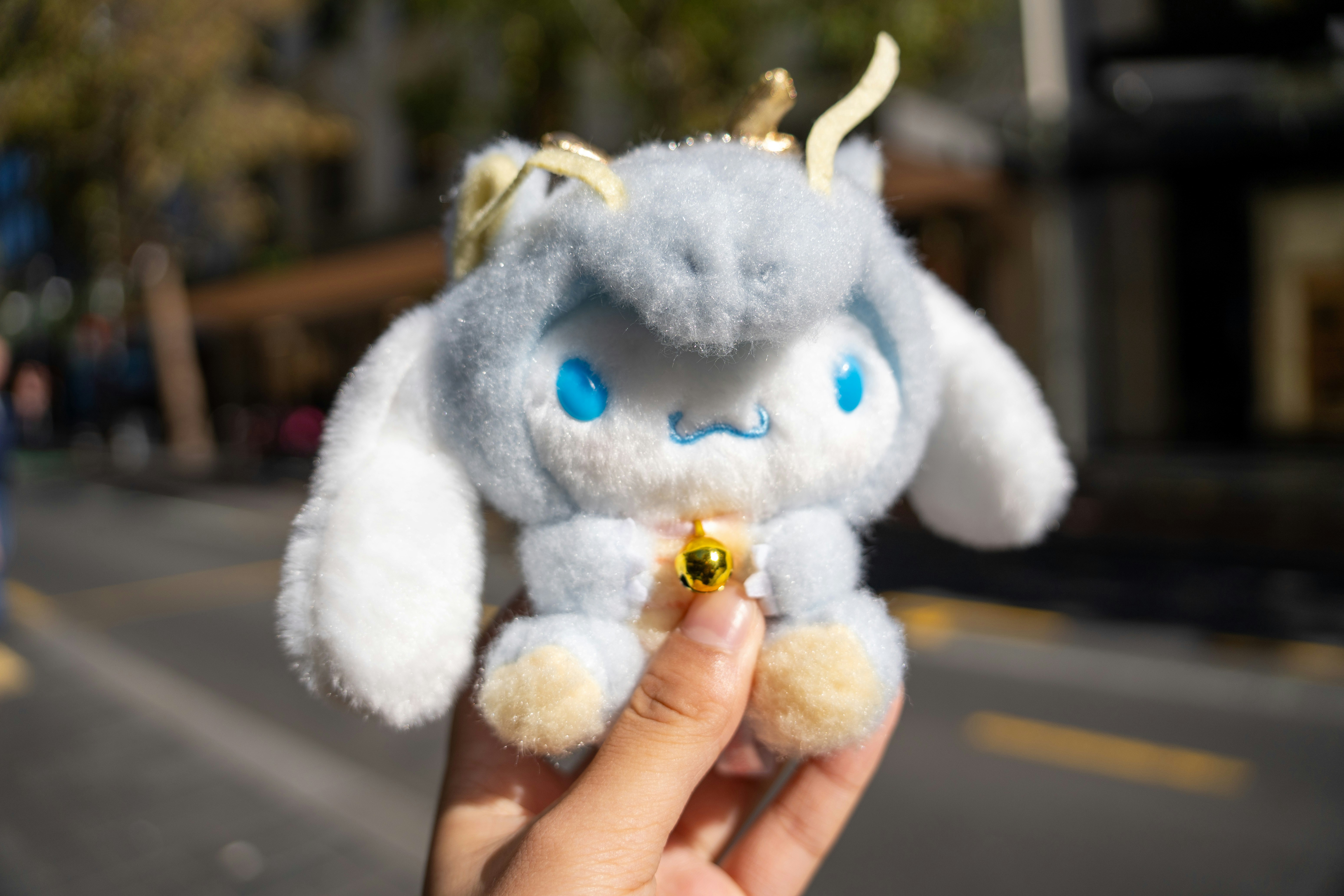 Blue-Eyed Plush Bunny Amid City Blur, Grasping a Tiny Golden Bell