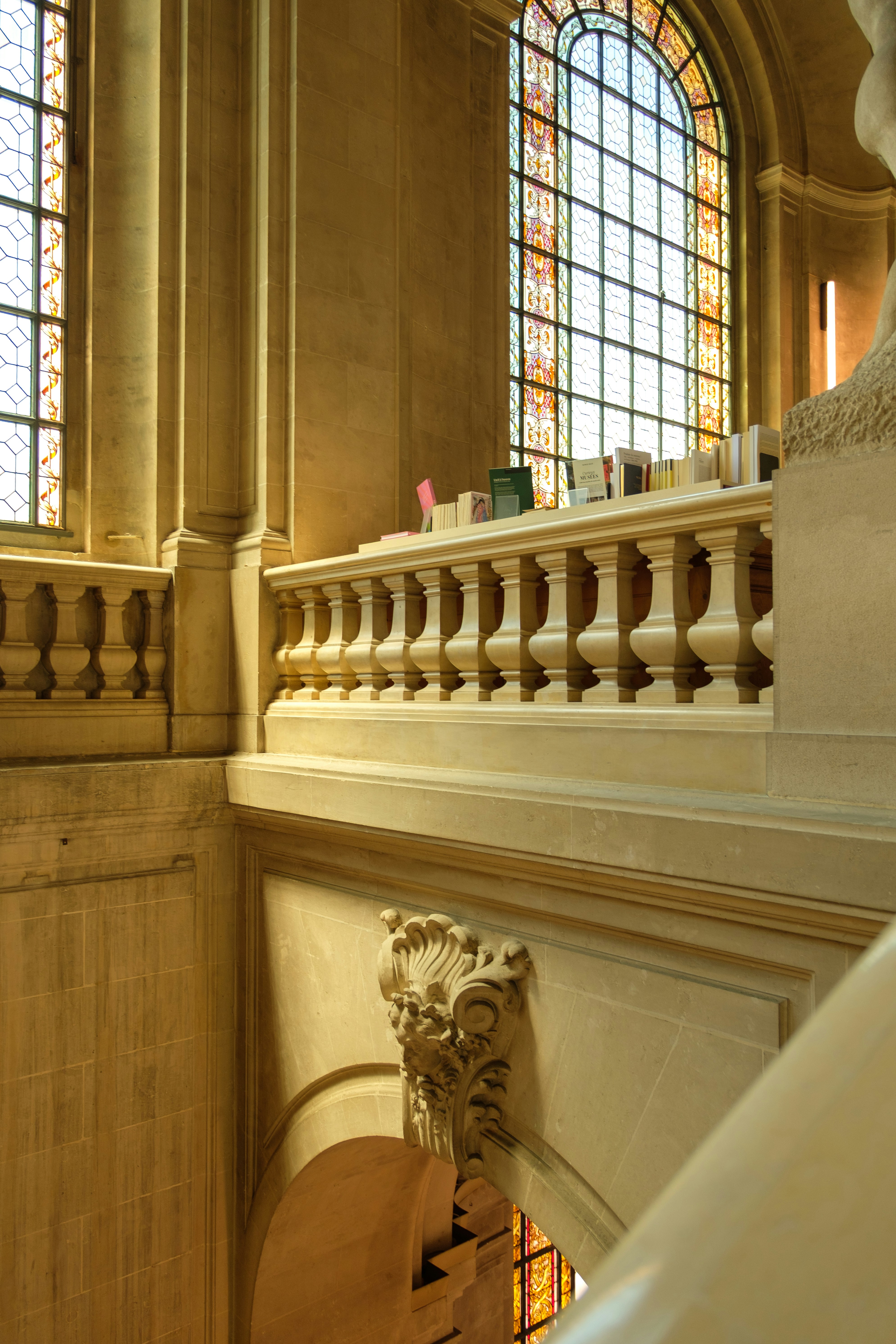 Intricate stonework and colorful stained glass enhance the serene atmosphere of a library's balcony, inviting quiet contemplation.