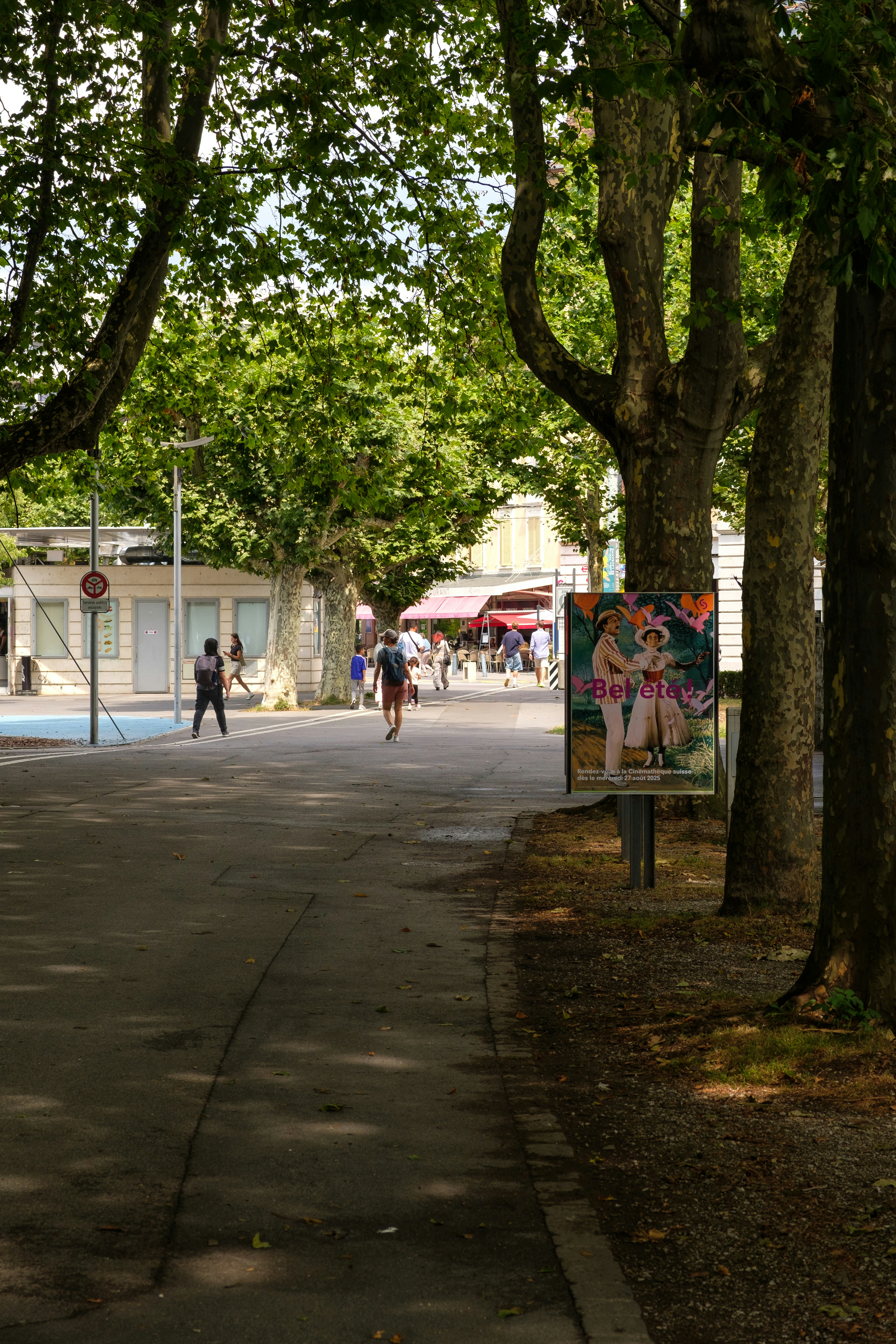 A shady street with people and a sign.