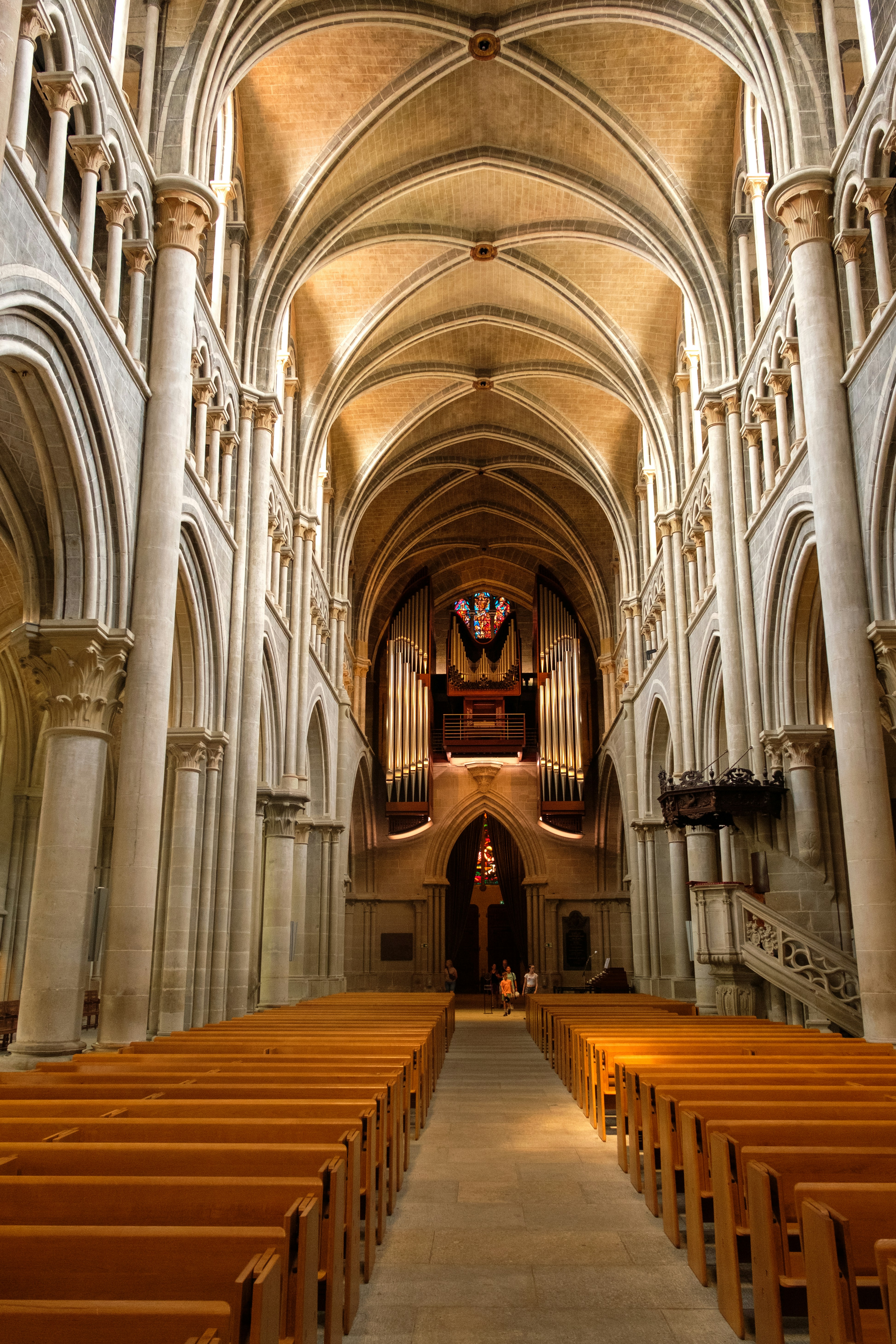 Interior of a grand cathedral showcasing soaring arches, wooden pews, and intricate stained glass above the altar.