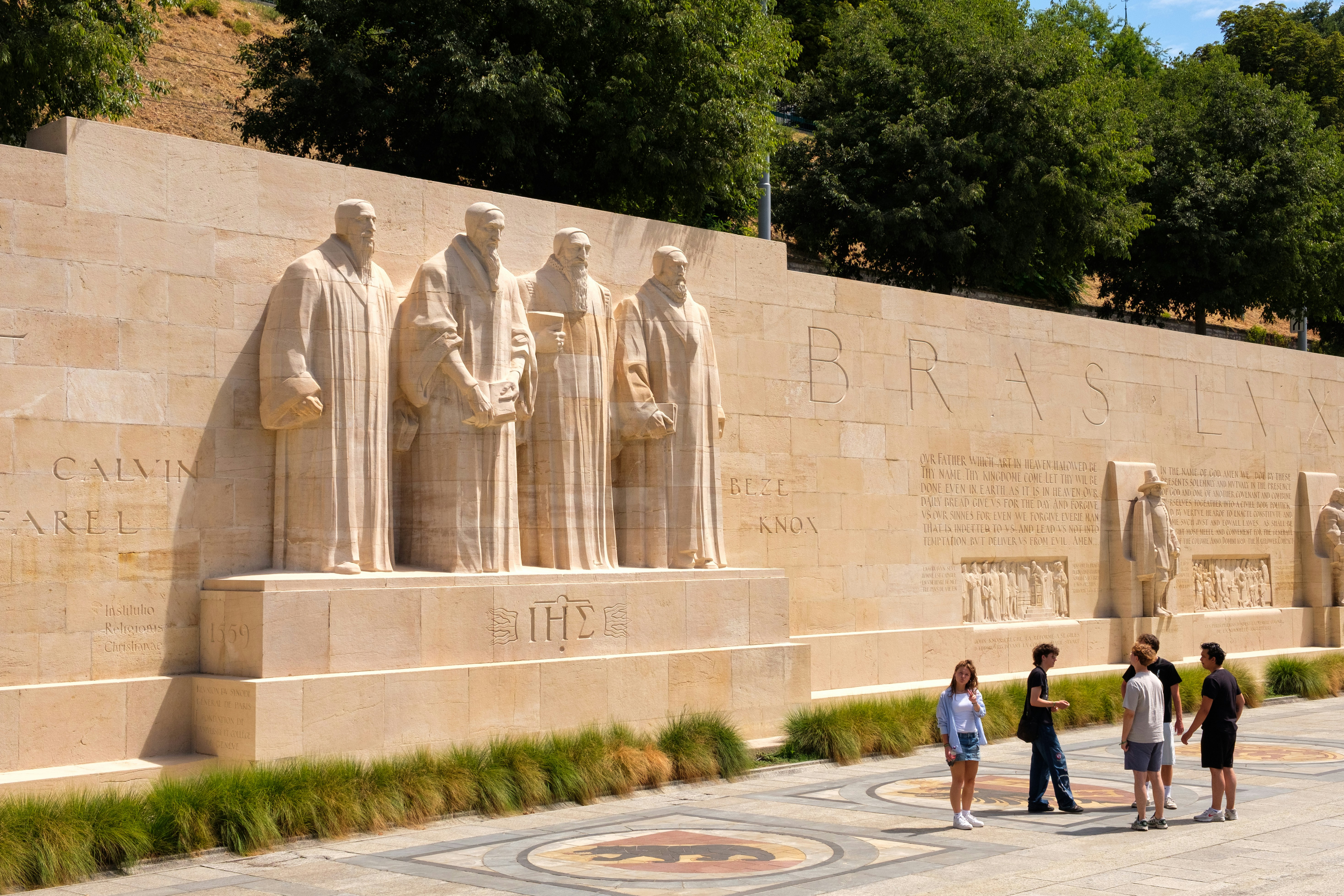 Imposing stone figures stand in solemnity against a textured wall, while visitors engage in thoughtful reflection below. 