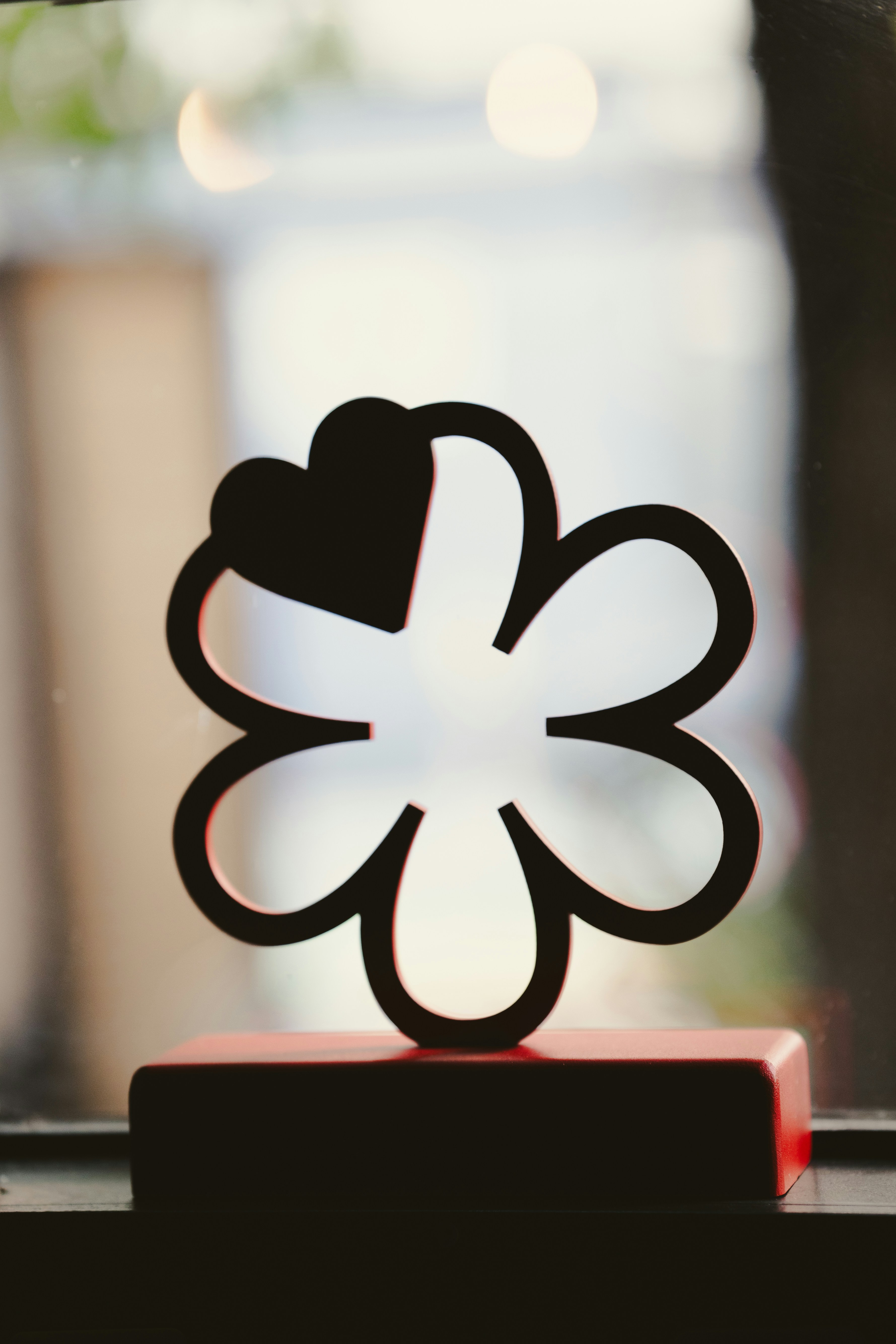 A playful flower-shaped sculpture with a heart detail, set against a softly blurred background. The piece exudes charm and warmth.