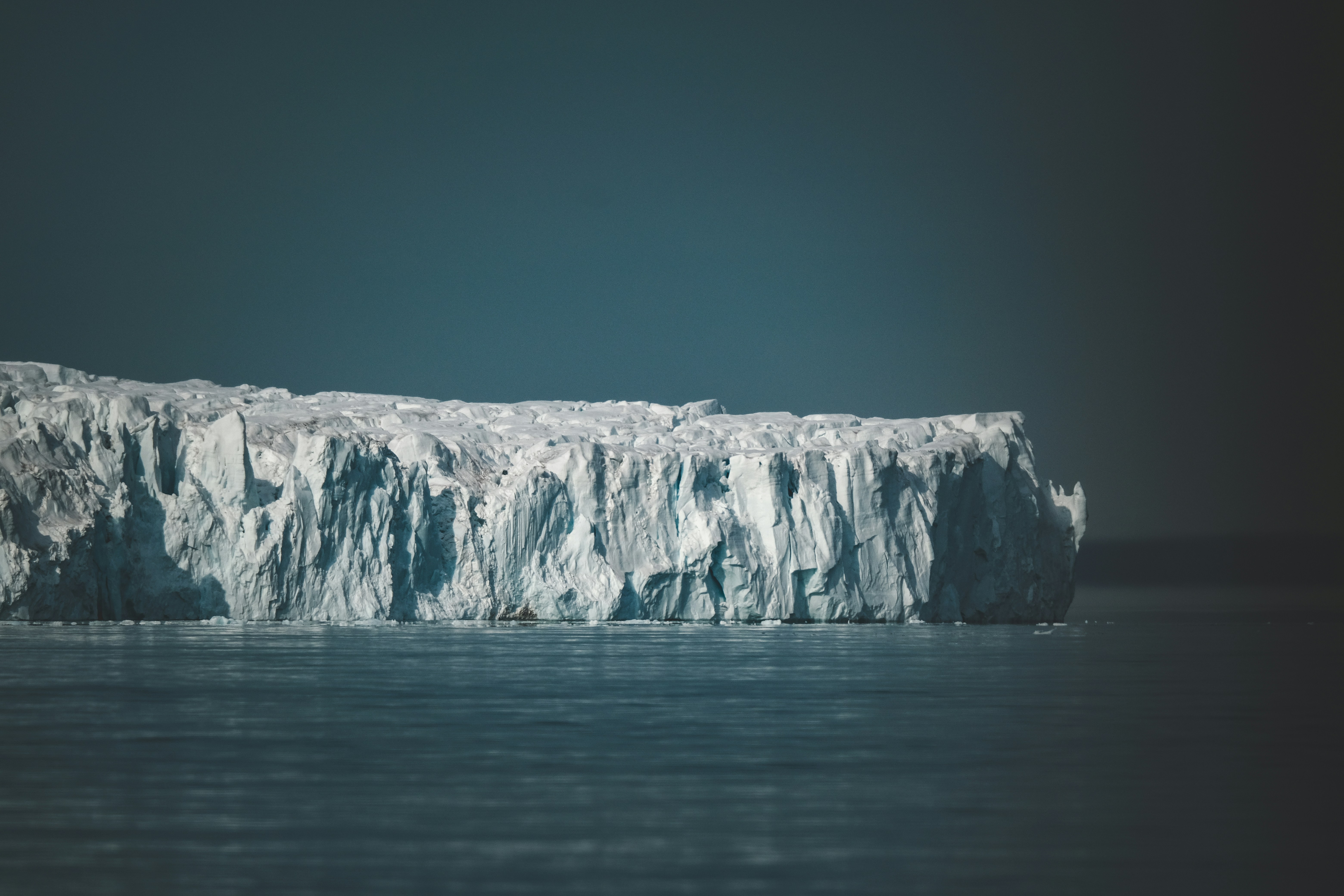 Massive glacier edge reflecting light on tranquil waters under a deep blue sky.