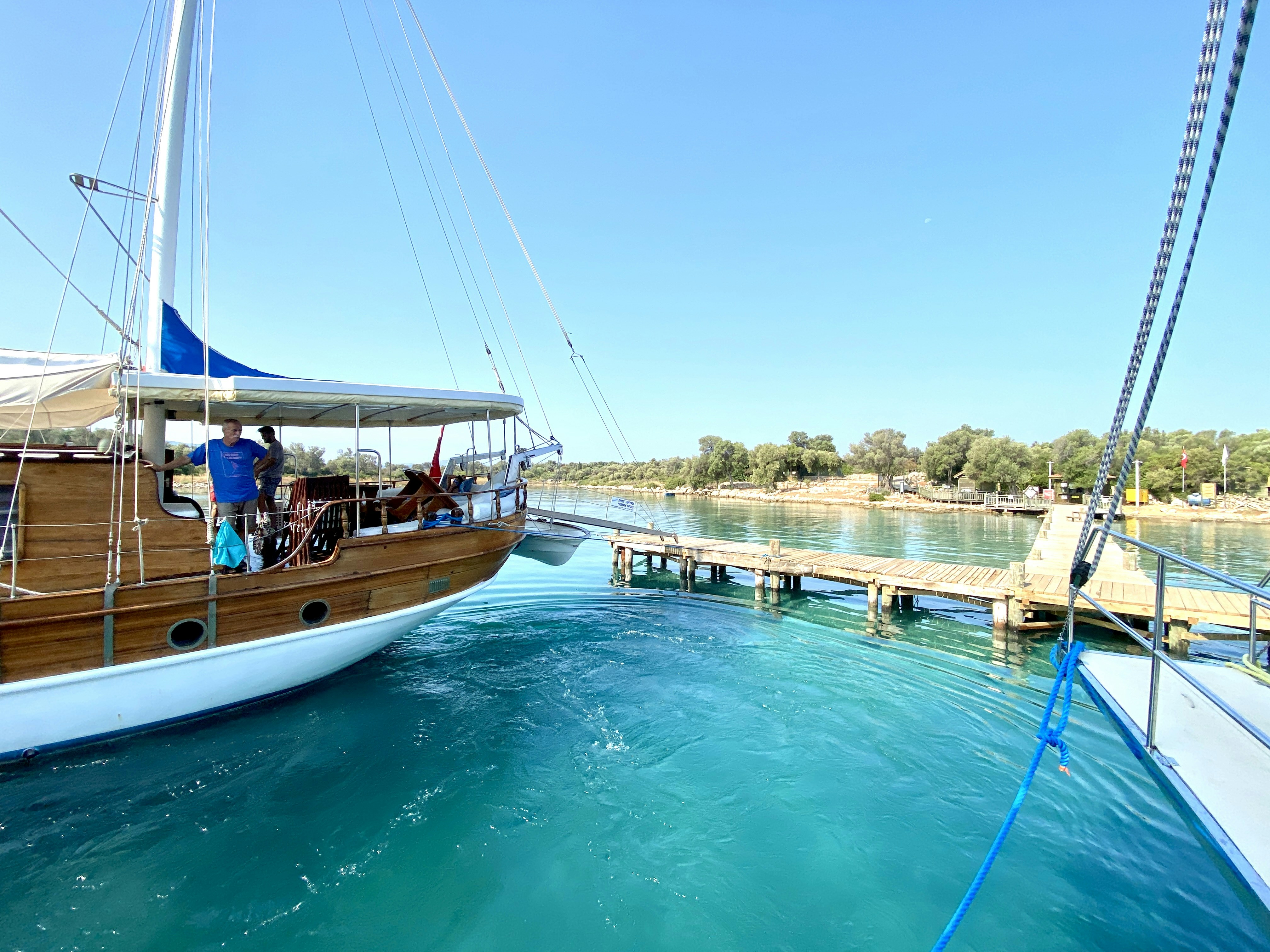 A sailboat docks on a pier in clear, turquoise water.