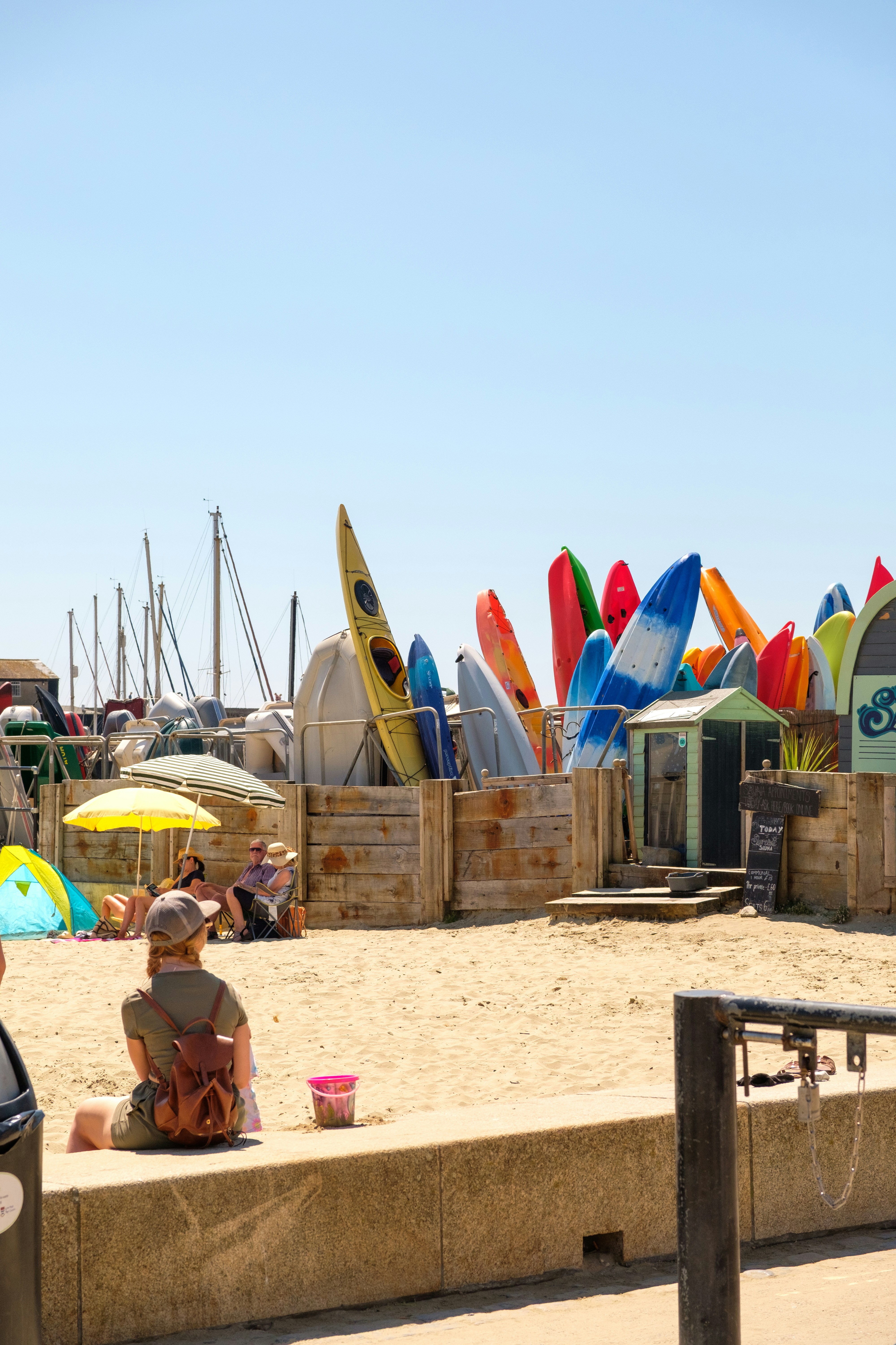 Colorful surfboards and beachgoers enjoying a sunny day at a coastal watersport hub. The scene captures the essence of summer leisure.