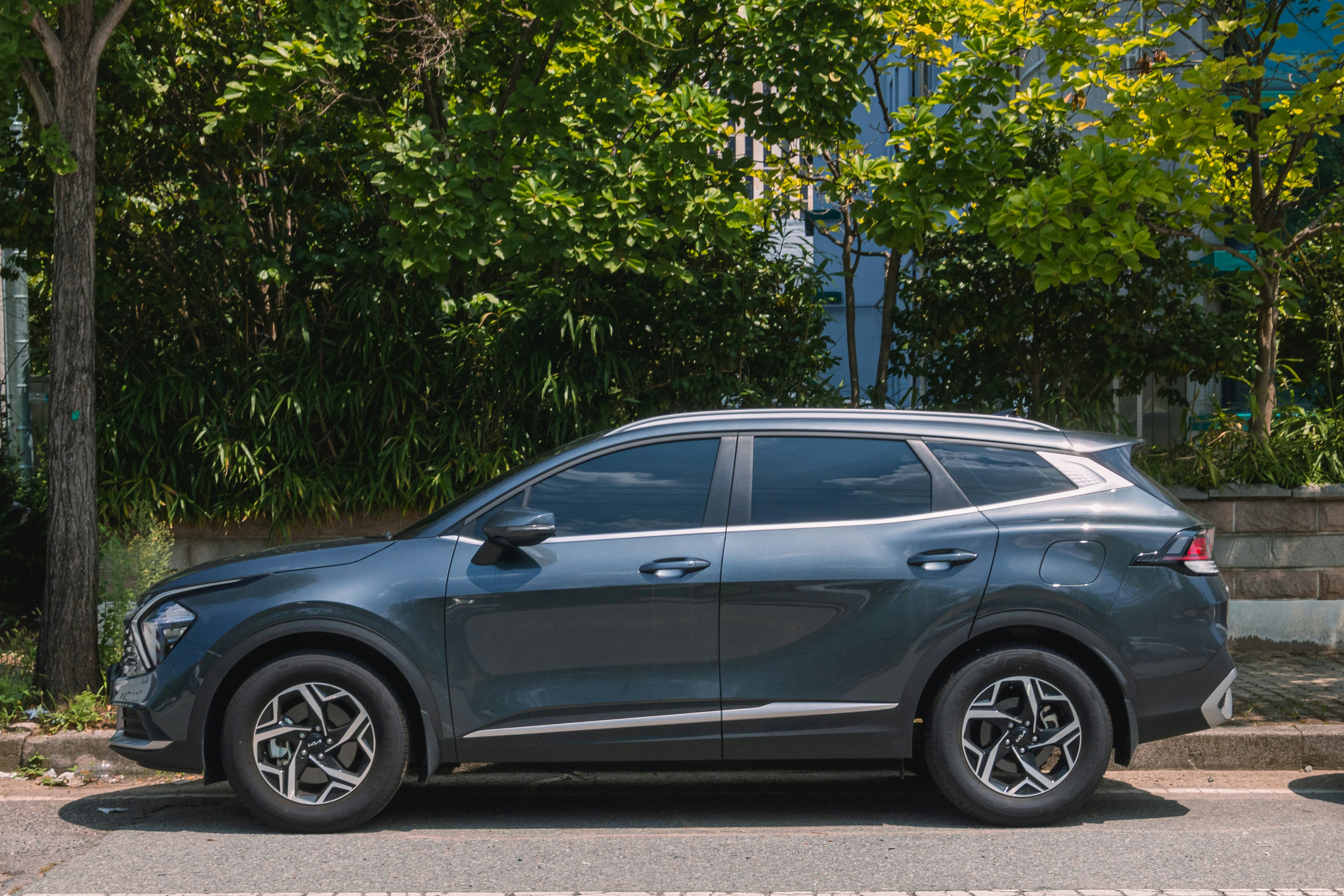 Sleek gray SUV parked beside lush greenery, showcasing its contemporary design against a vibrant urban backdrop.