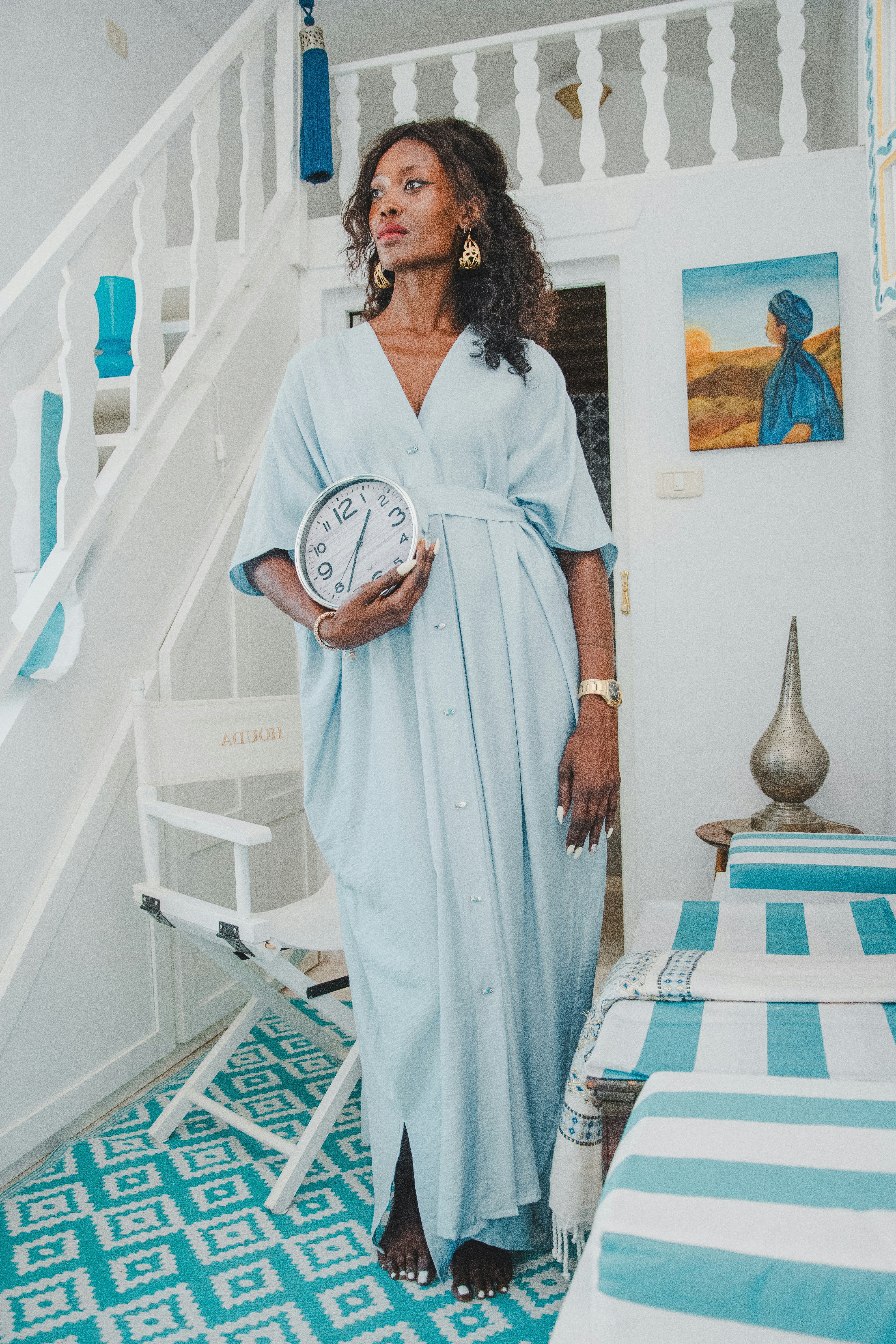 Fashion portrait of a gorgeous black model holding a watch. | A woman poses holding a clock, wearing a dress.