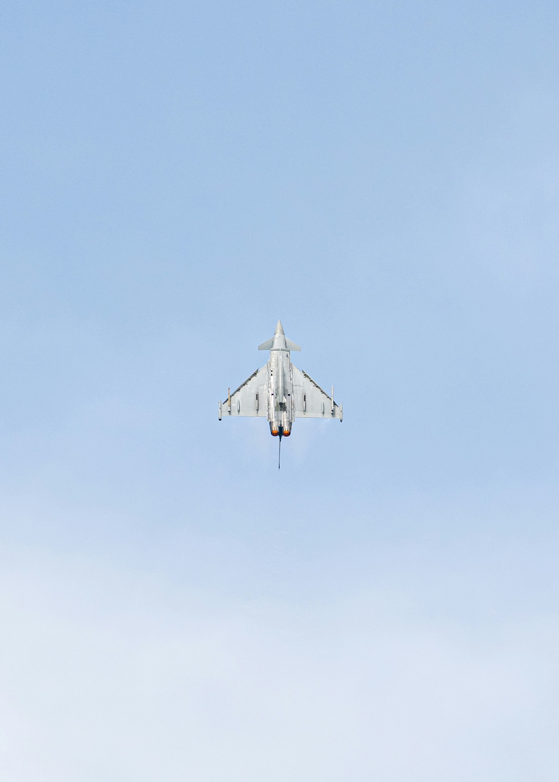 Military jet soaring against a pale blue sky, showcasing aerodynamic design and engineering prowess.