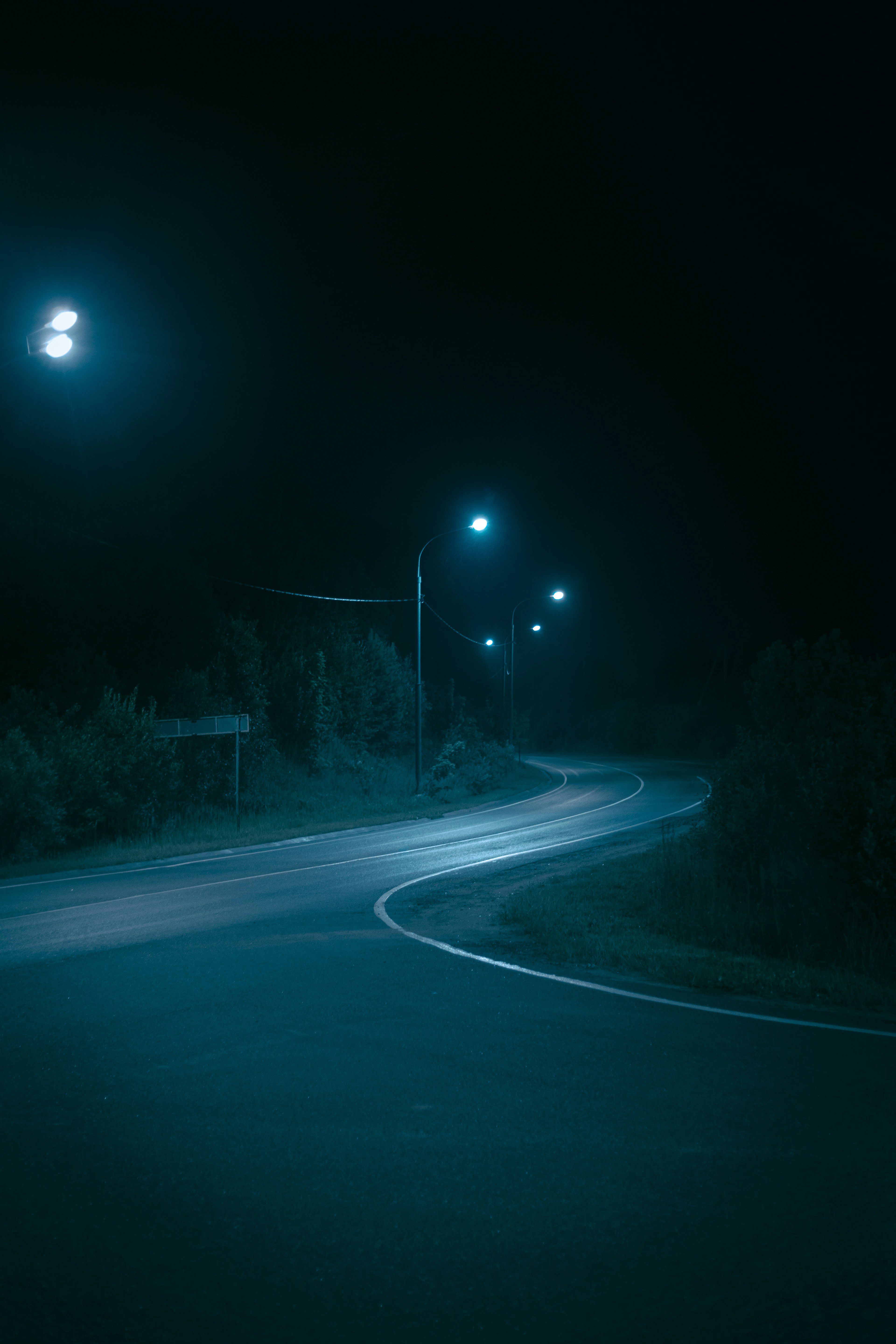 A curving road lit by gloomy streetlamps at night.
