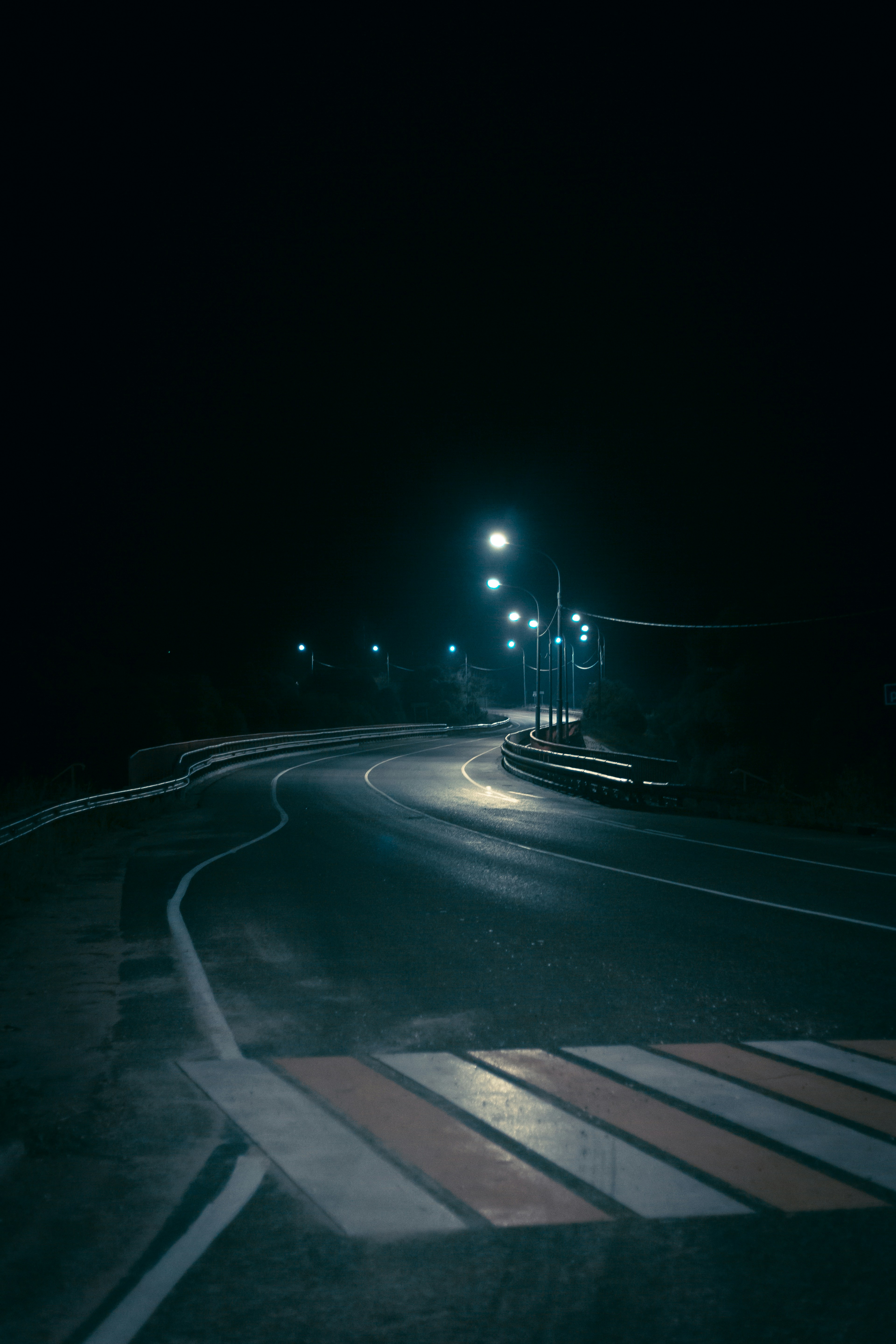 Empty road curves at night with streetlights.