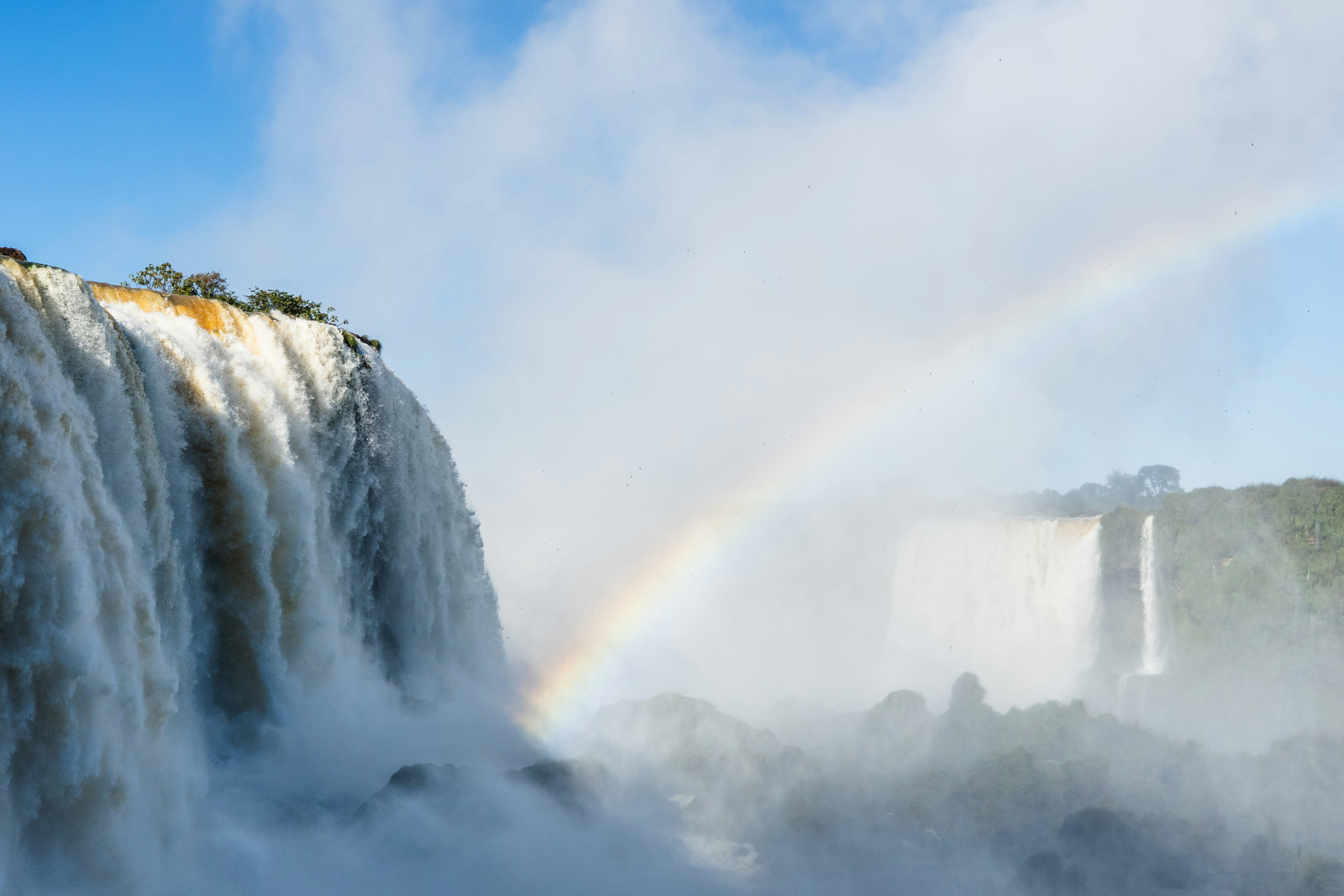Majestic waterfalls cascading amidst mist, with a vibrant rainbow arching across the scene.
